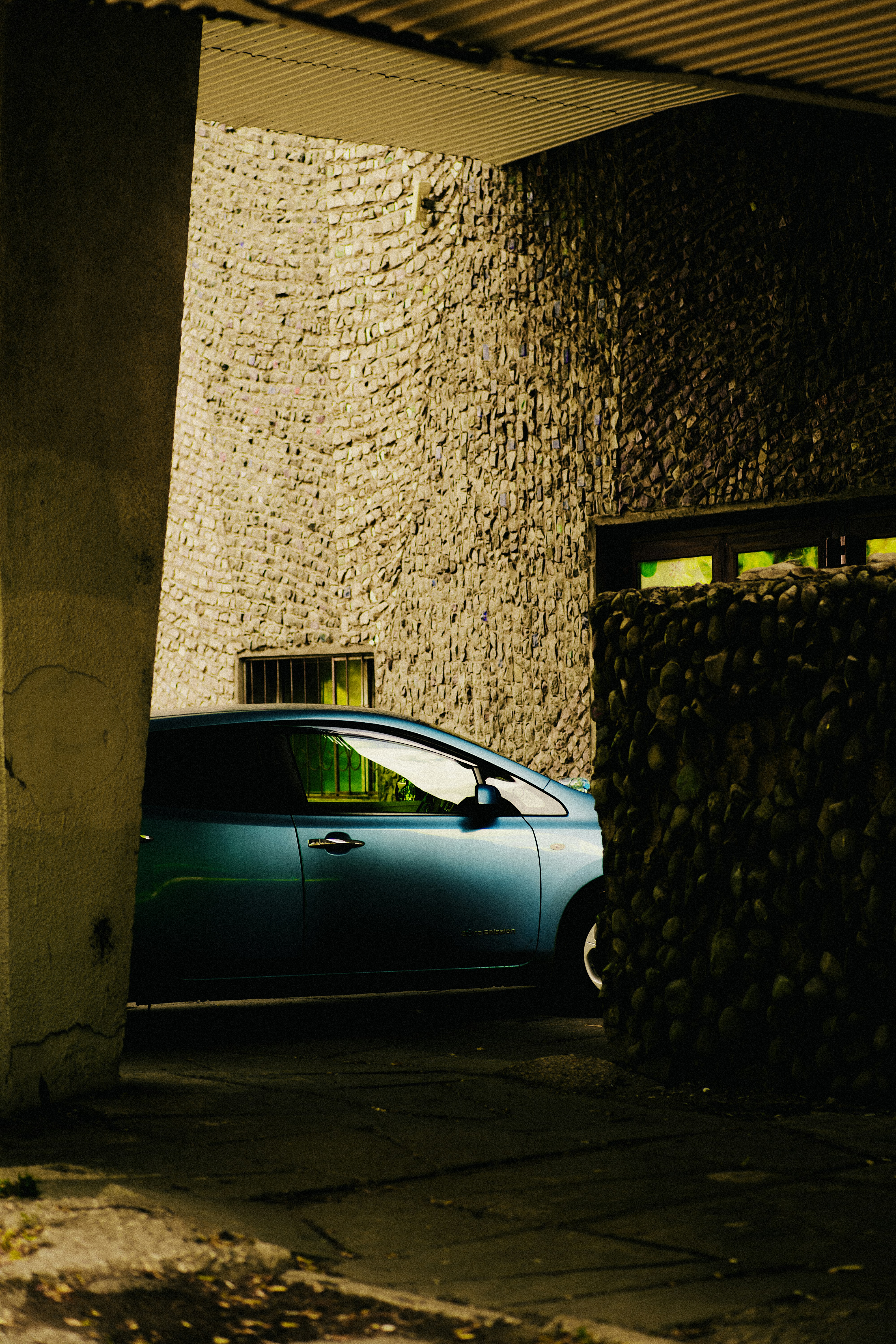 Whispered Reflections: A Blue Hatchback in a Stone-Walled Courtyard