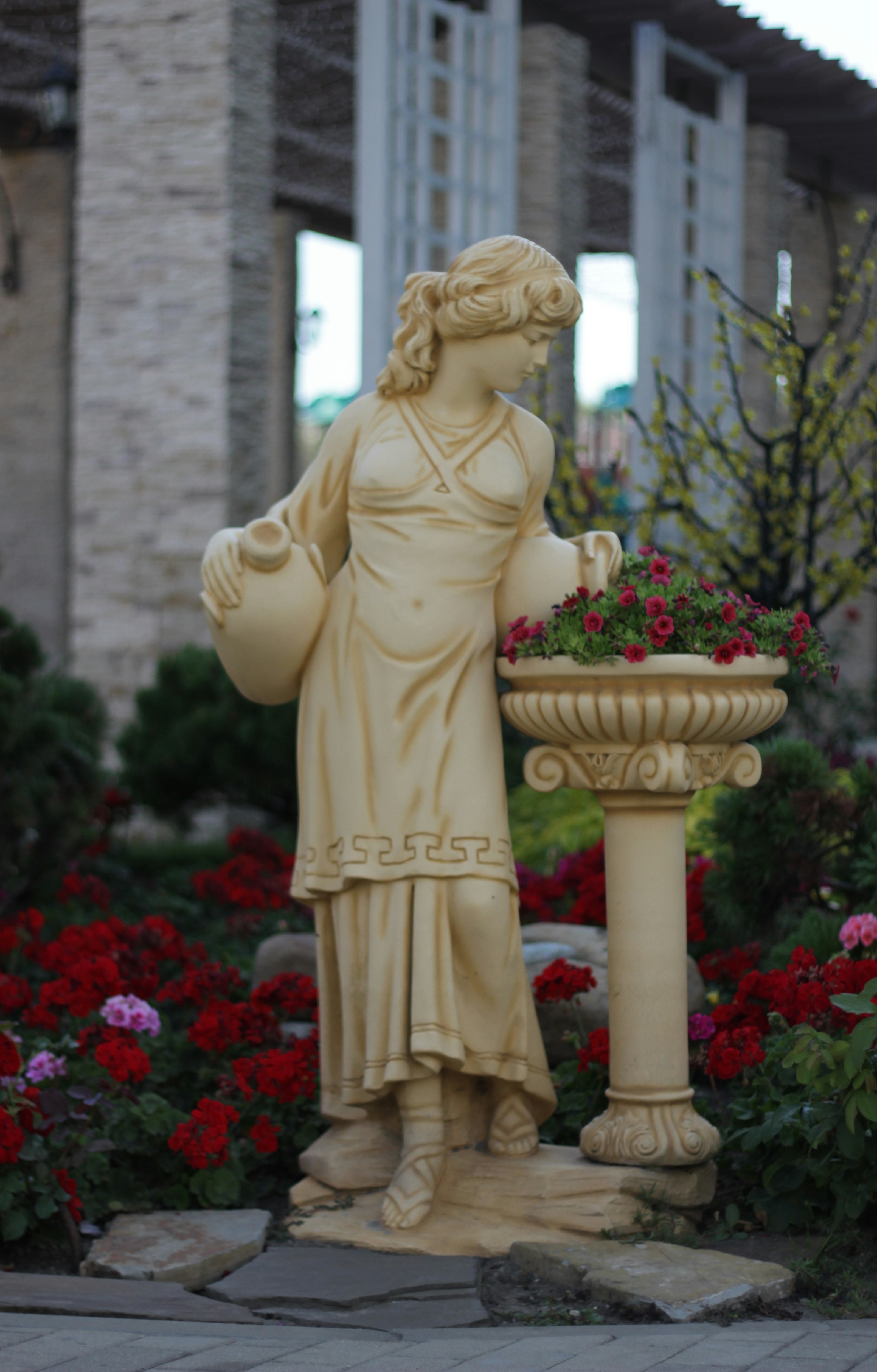 Cream-Colored Statue Tending a Vessel Amid a Crimson Flower Garden