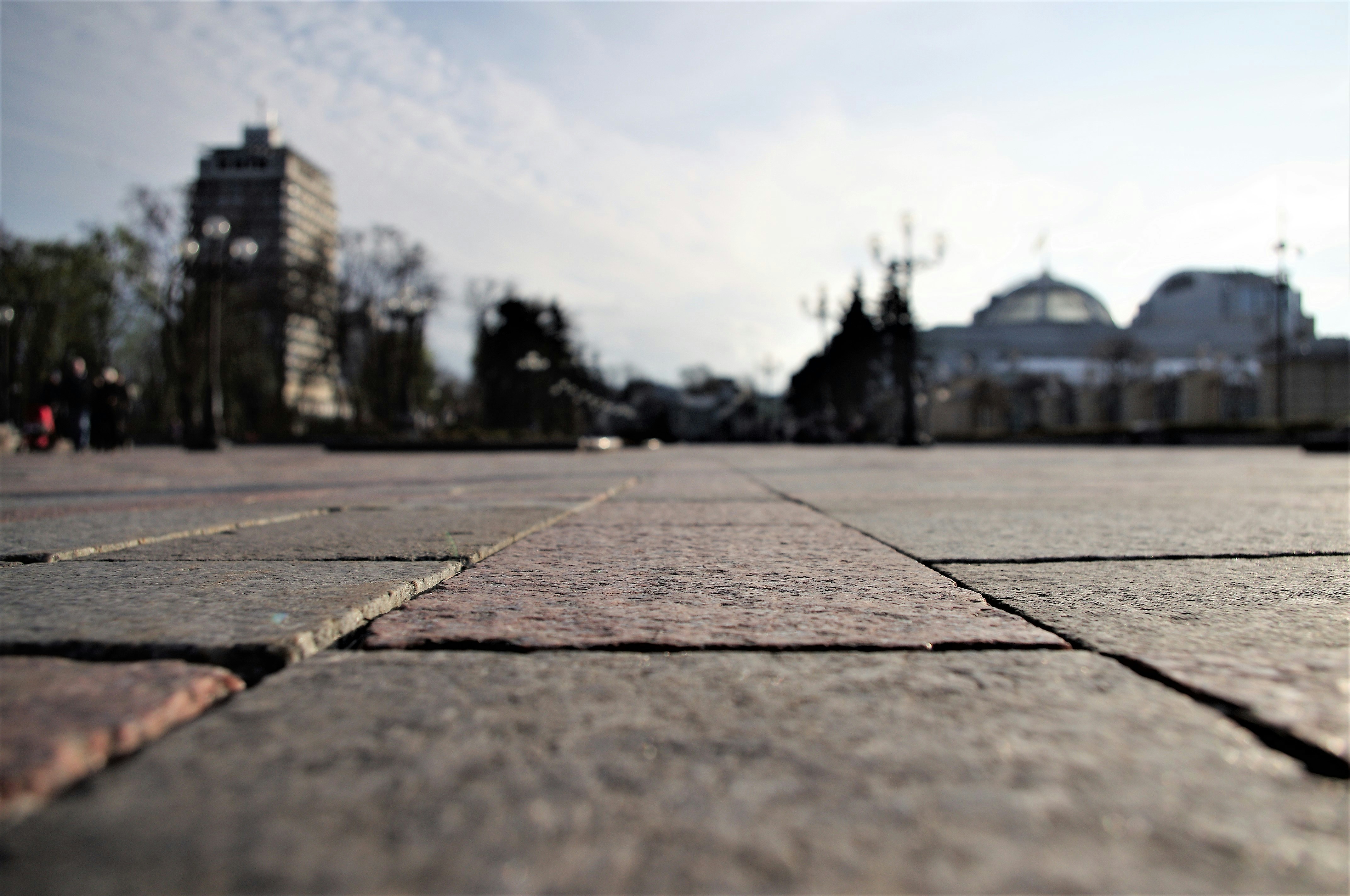 Low-angle shot of a tiled plaza leading toward a distant cityscape; brick textures dominate the foreground with a soft, shallow depth of field toward the background. This is a ground-level architectural/environmental capture.