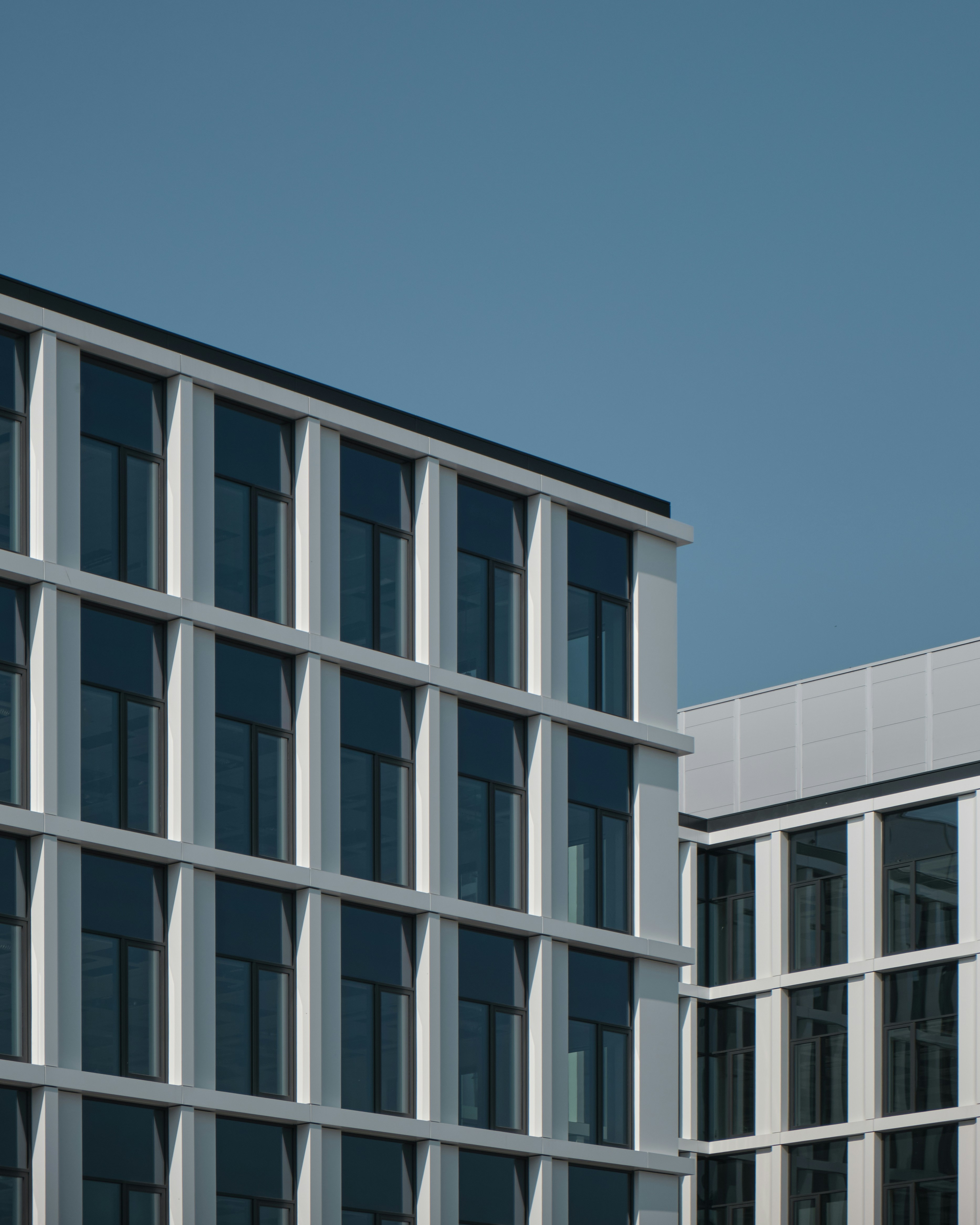 Modern office buildings with grid-like window patterns against a clear blue sky.