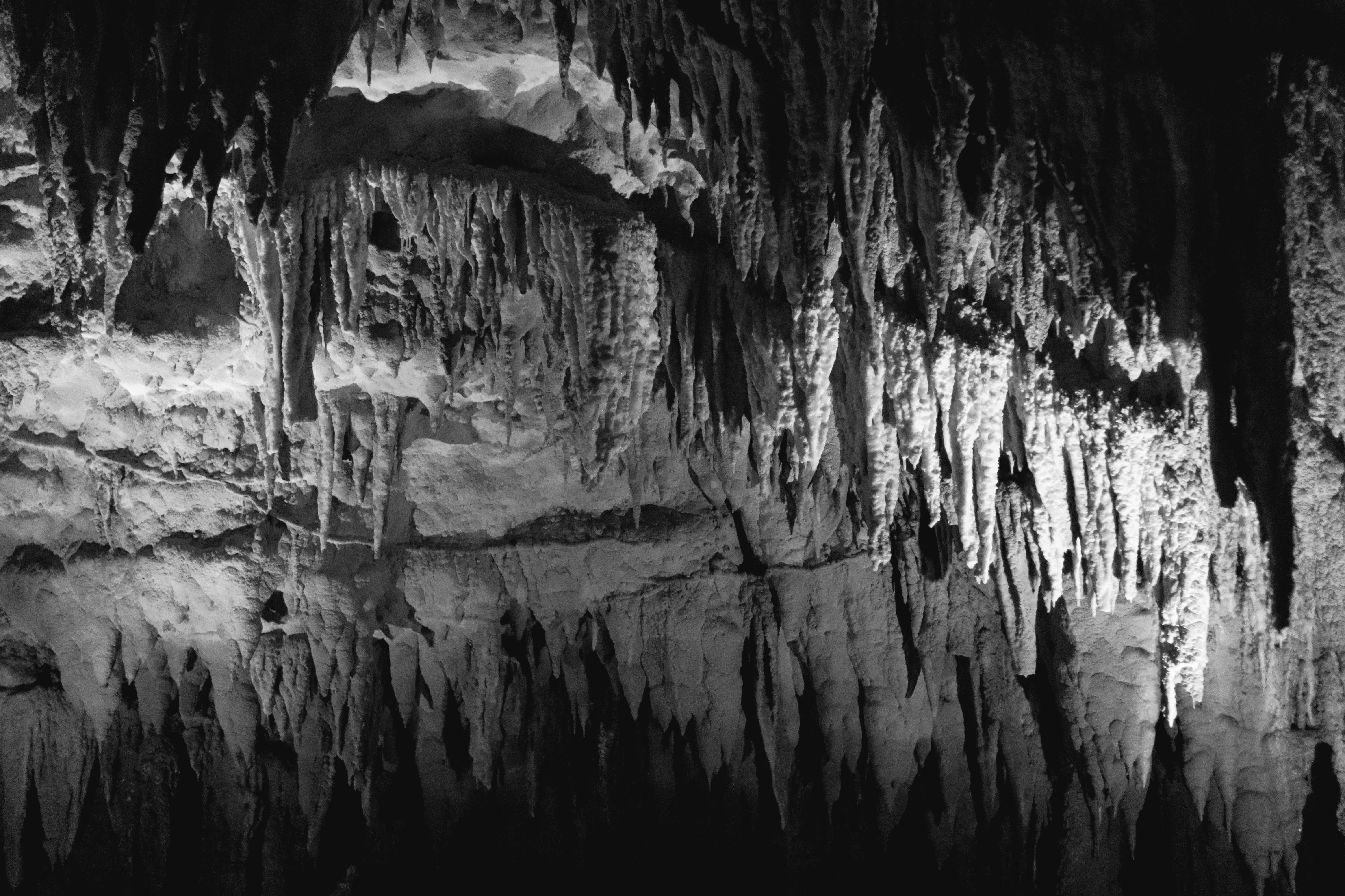Intricate stalactites hang from the cavern ceiling, illuminated by subtle lighting that accentuates their textures and formations.