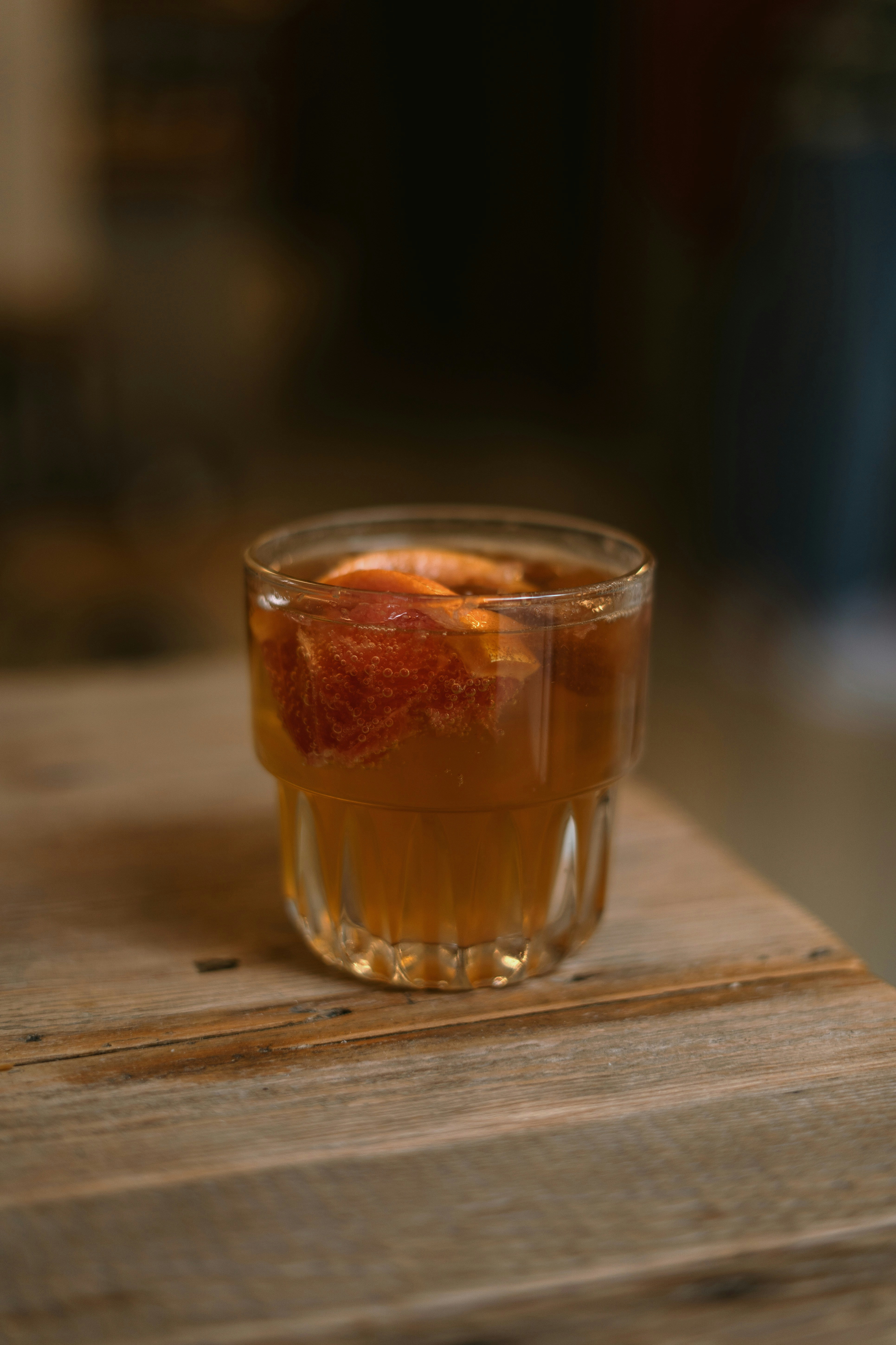 Glass of amber cocktail garnished with citrus slices on a wooden surface.