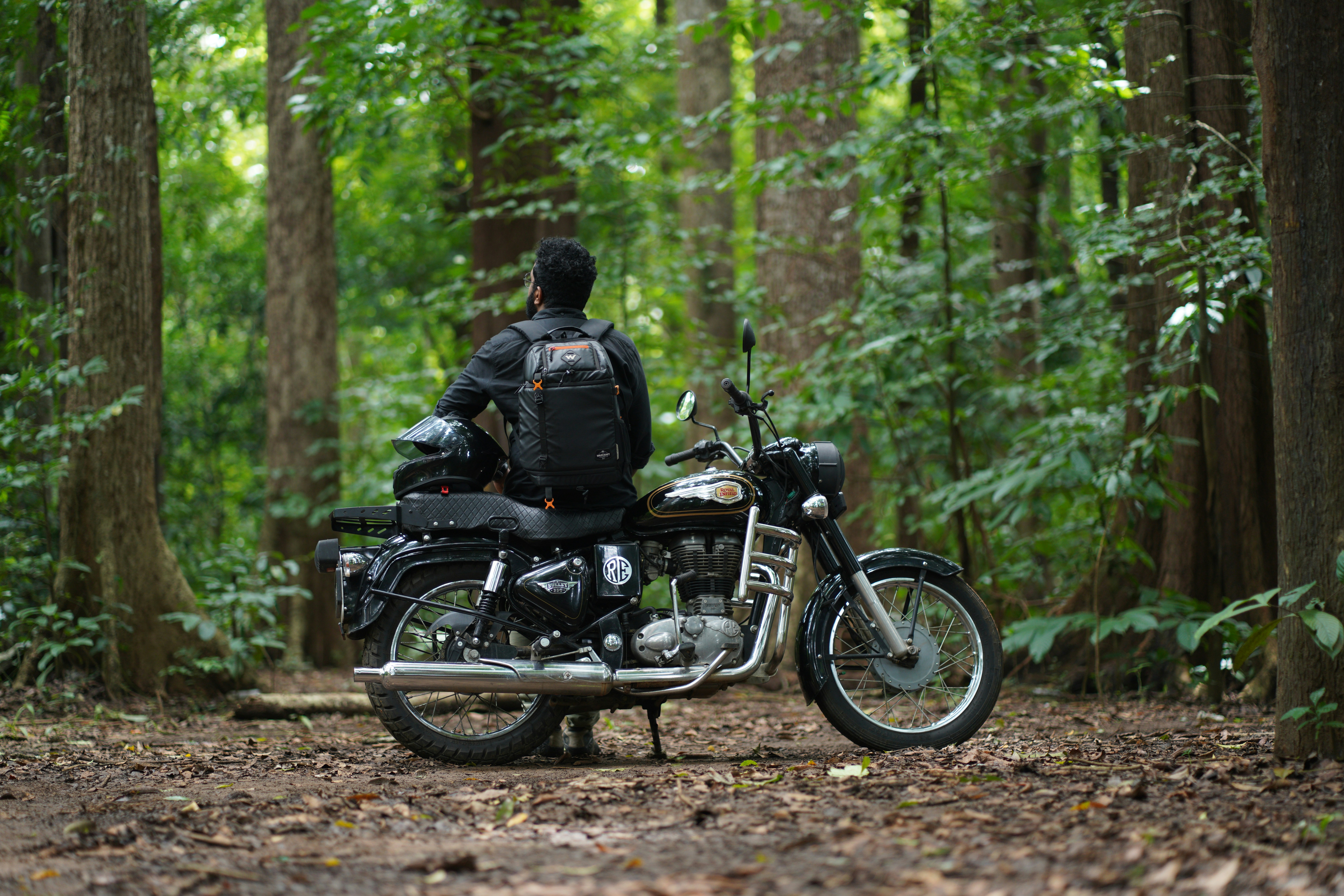 Motorcyclist pausing in a lush, green forest surrounded by towering trees.