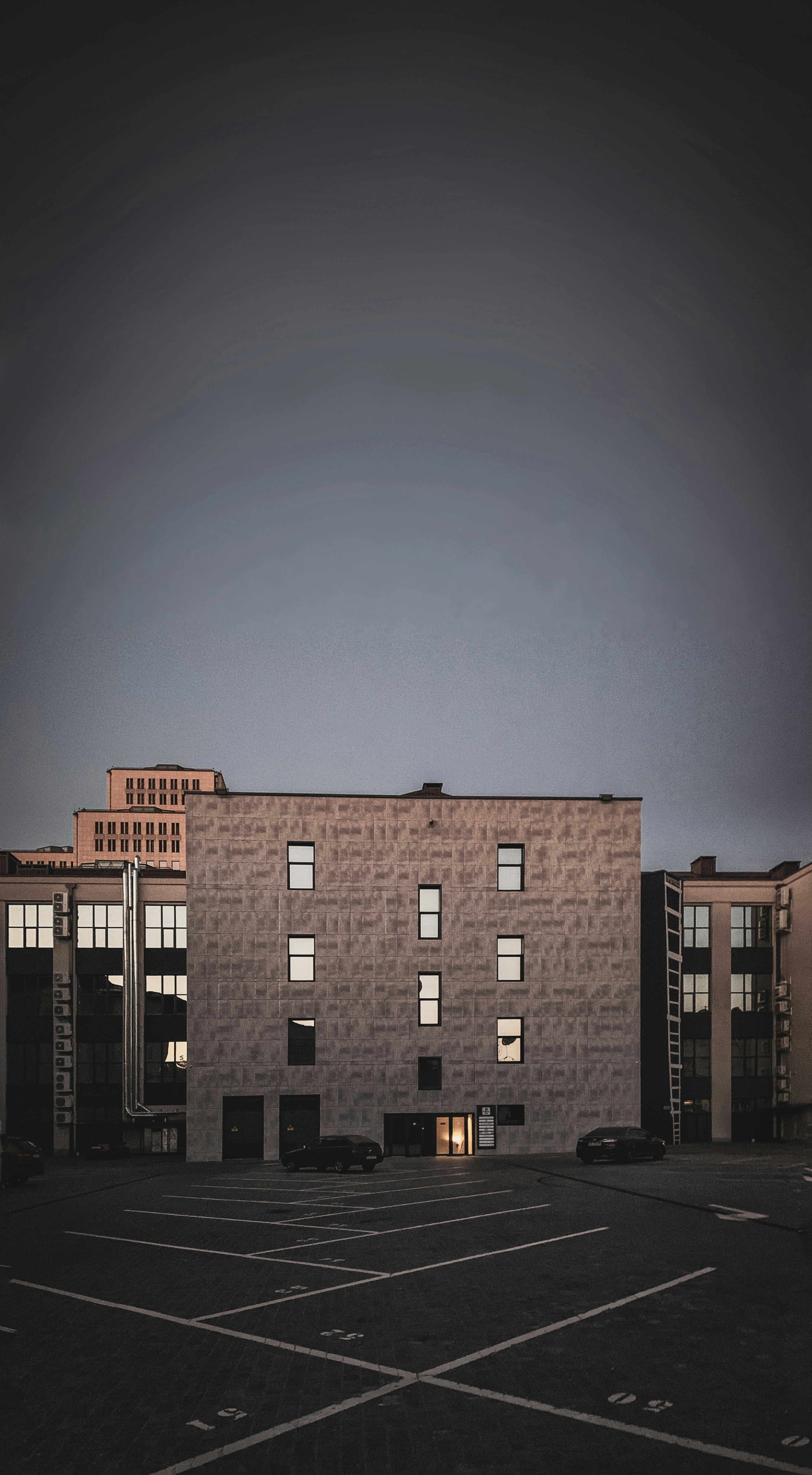 The Quiet Monolith: Central Brick Block in a Dusk-Blue Parking Lot