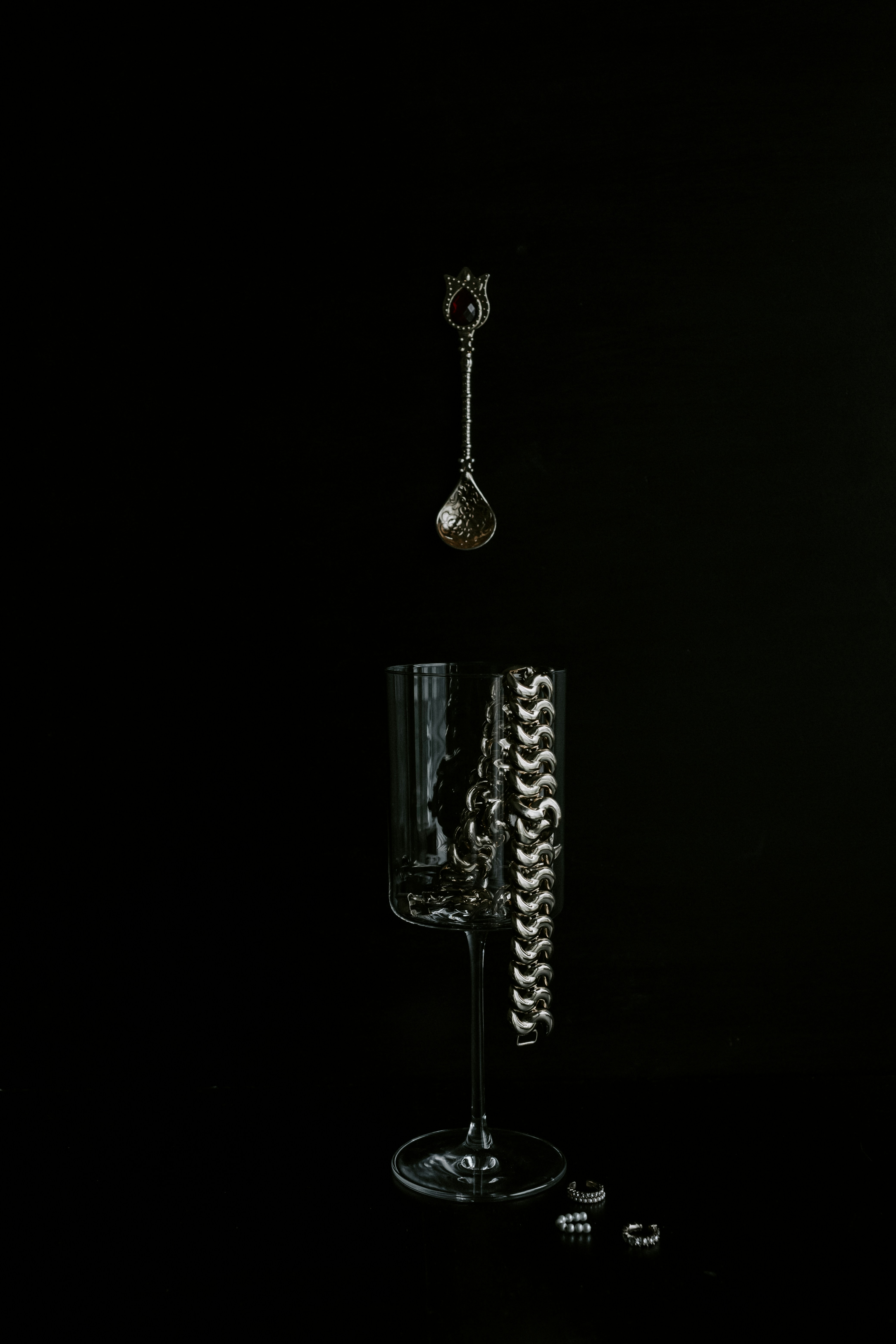 Crystal Teardrop Suspended Over a Chain-Draped Goblet in a Noir Studio