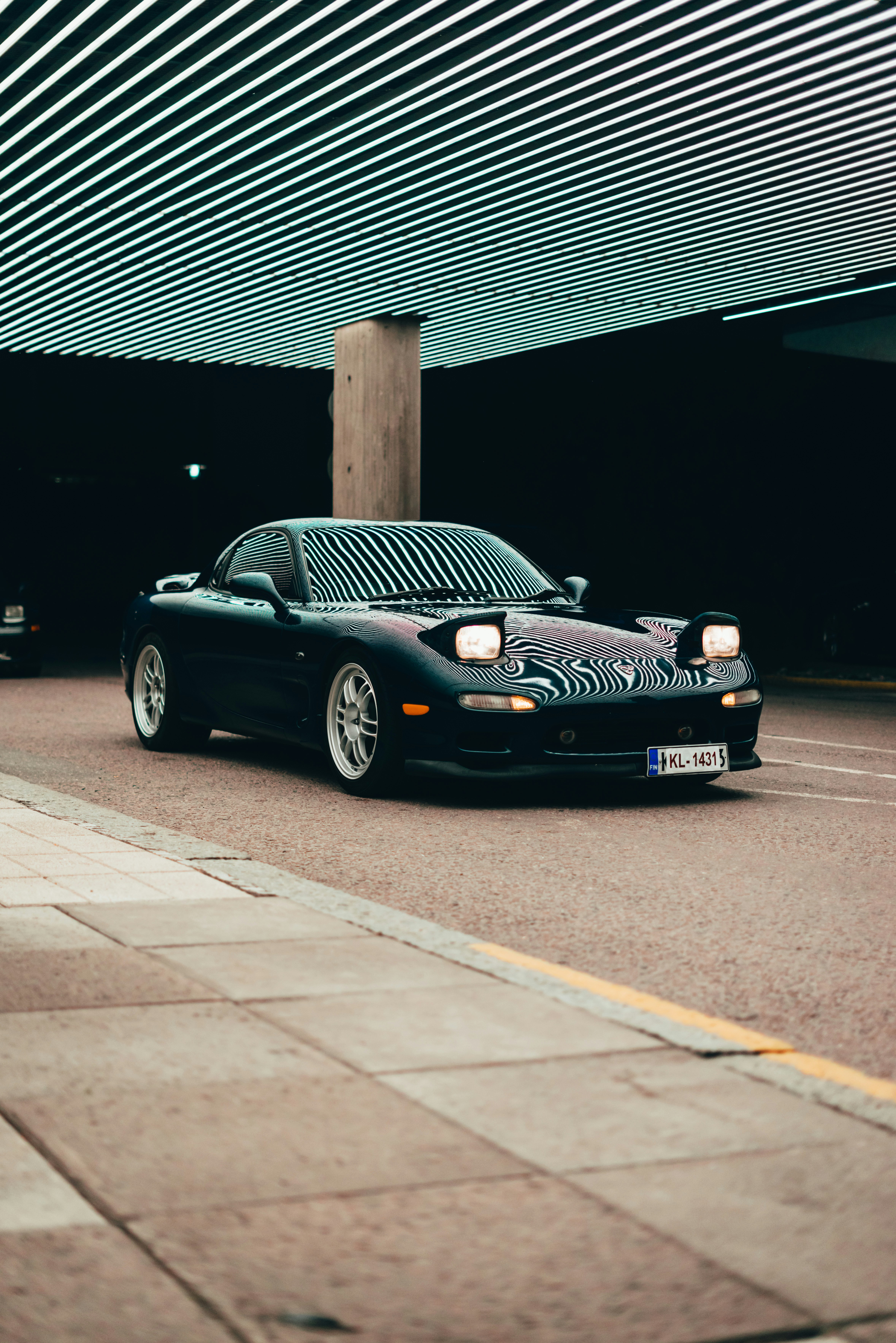 Mazda RX-7 parked beneath a striking striped ceiling, showcasing its sleek design and modern urban setting.