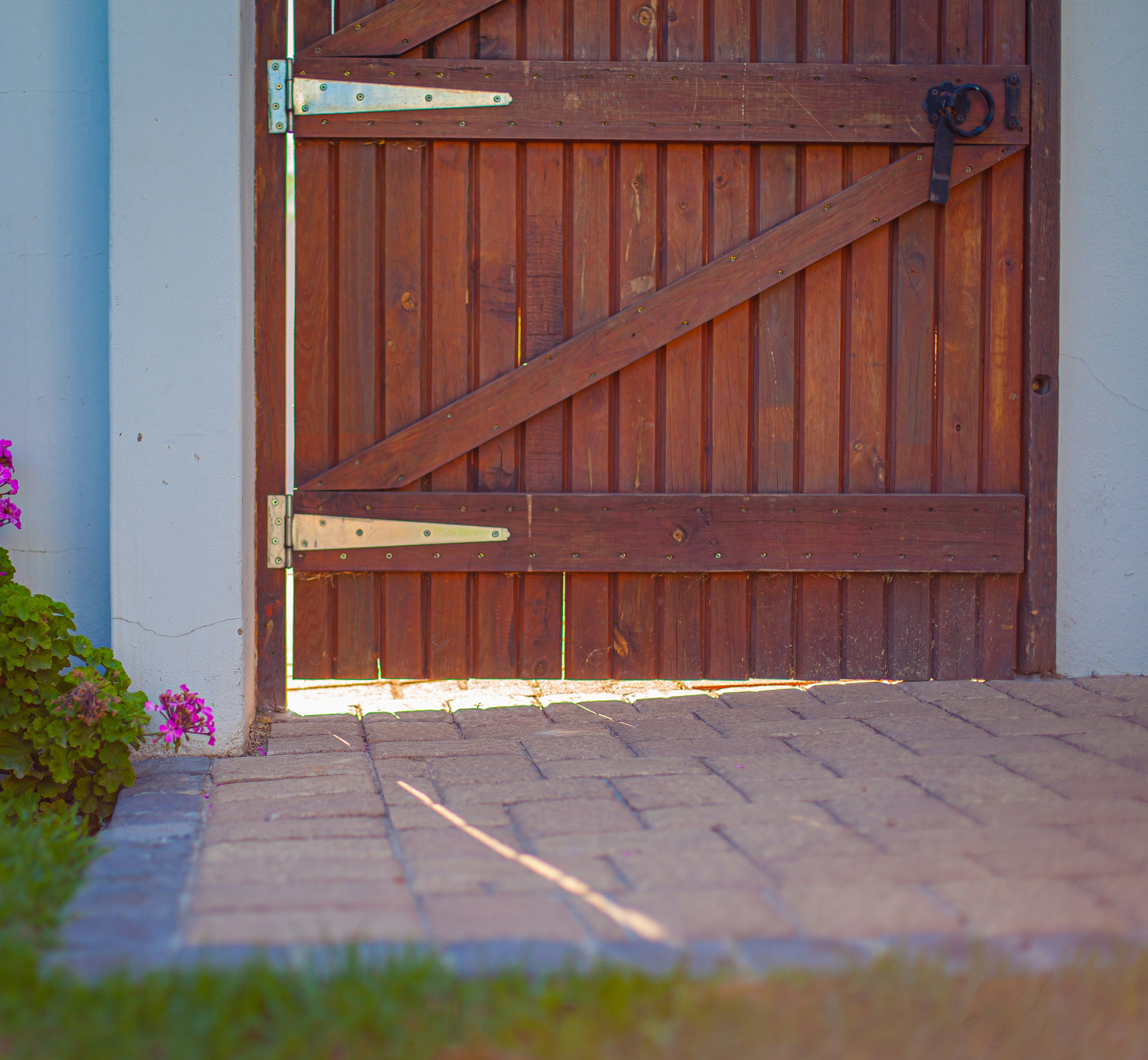 Wooden gate with diagonal slats, partially open, surrounded by vibrant flowers and stone pathway.