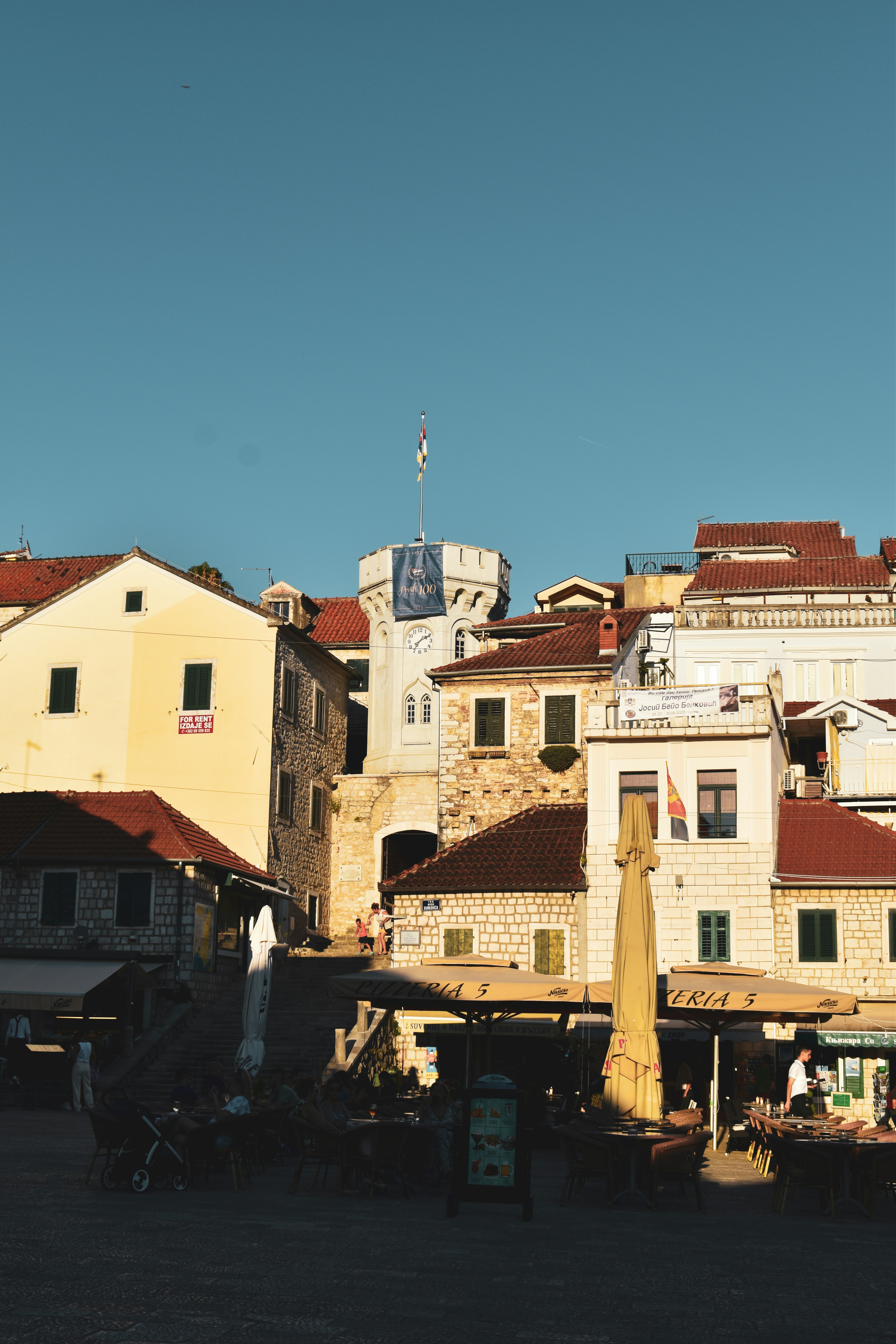 Sunlit Piazza: A Flag-Topped Clock Tower Surrounded by Terracotta Rooftops