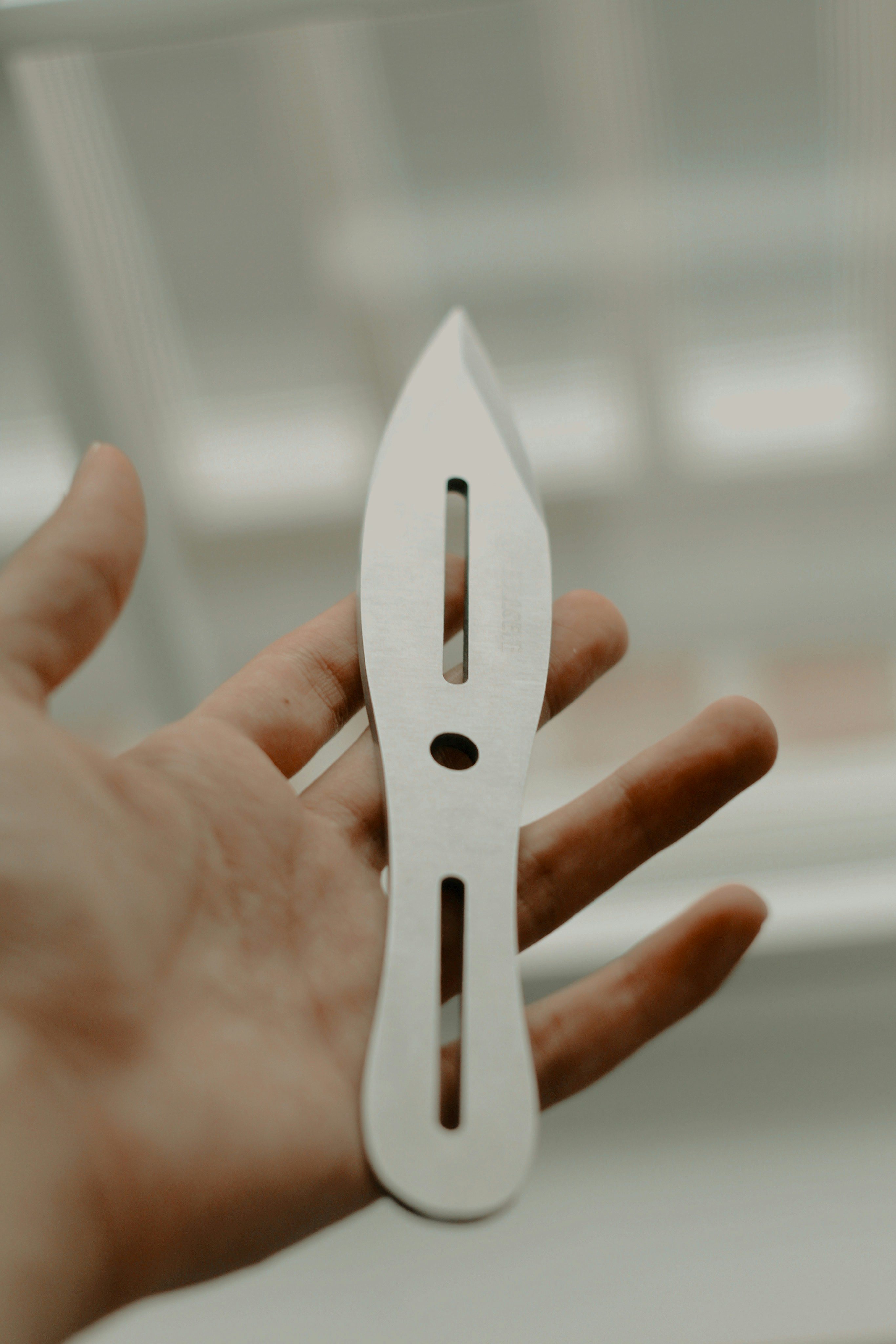 A hand holds a sleek, metallic scalpel blade against a softly blurred background, emphasizing its sharpness and design.