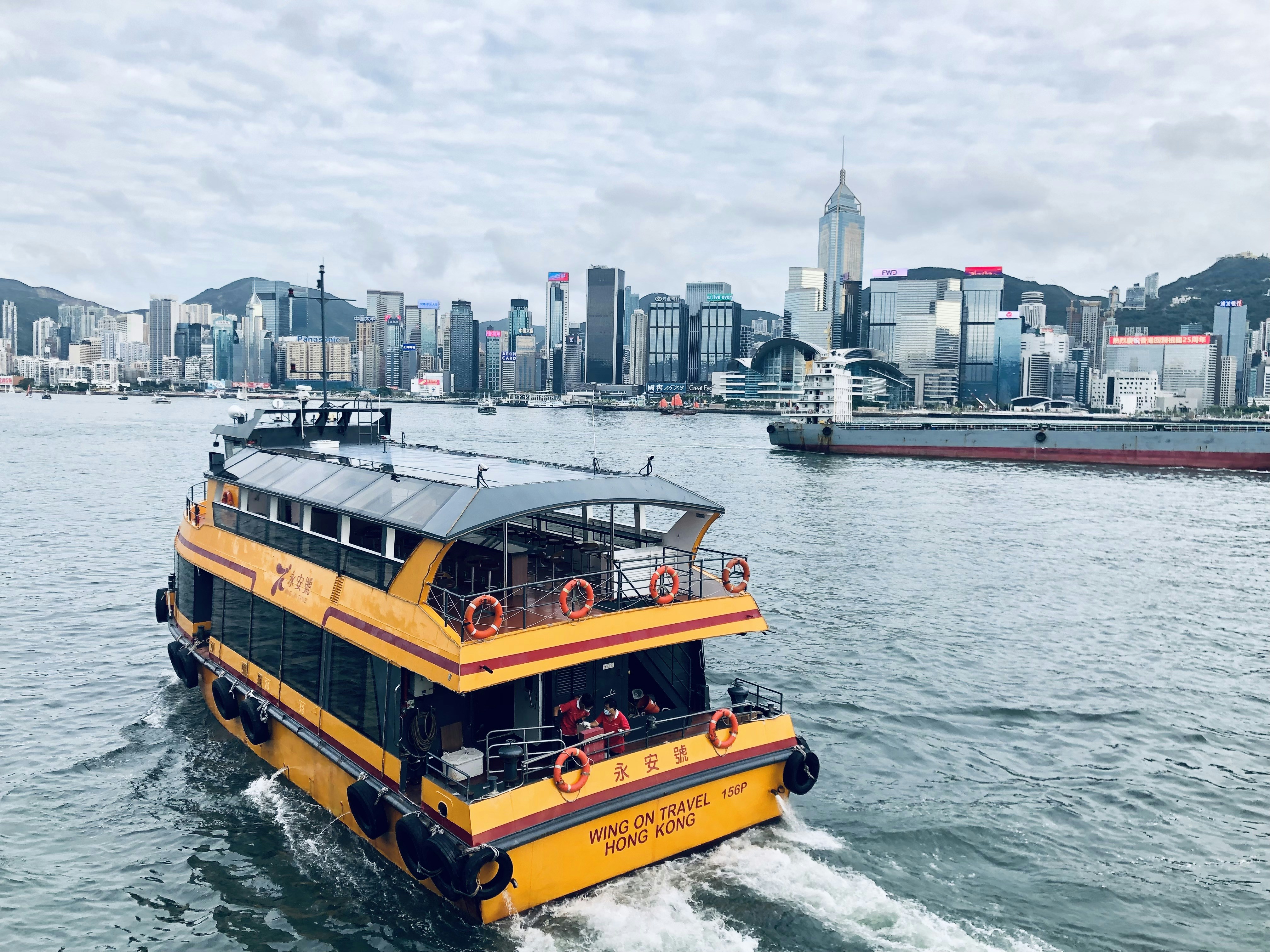 Yellow double-decker ferry slicing through Hong Kong harbor toward a steel-blue skyline