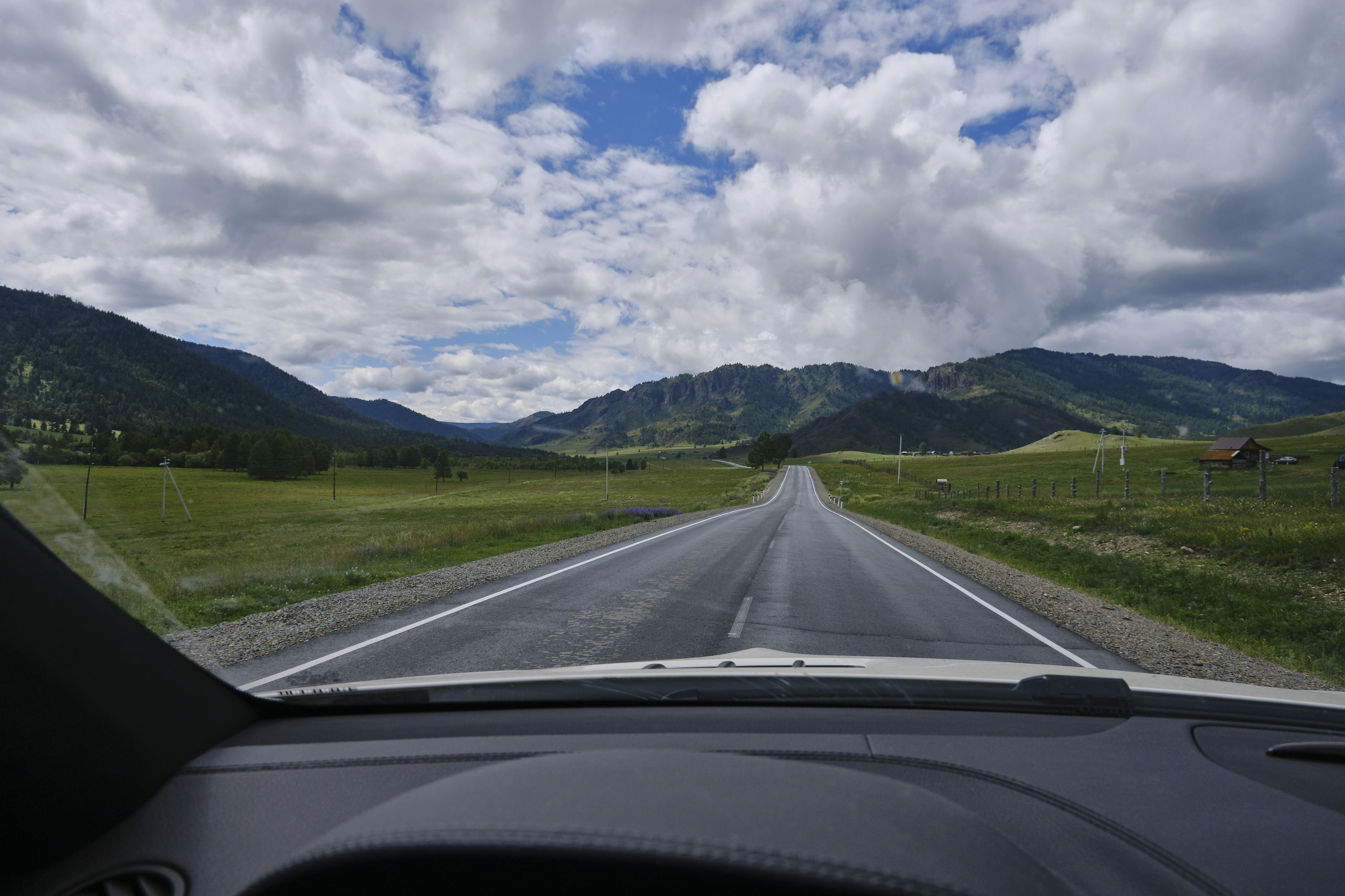 Vanishing Road through Emerald Valleys under a Cloud-kissed Sky