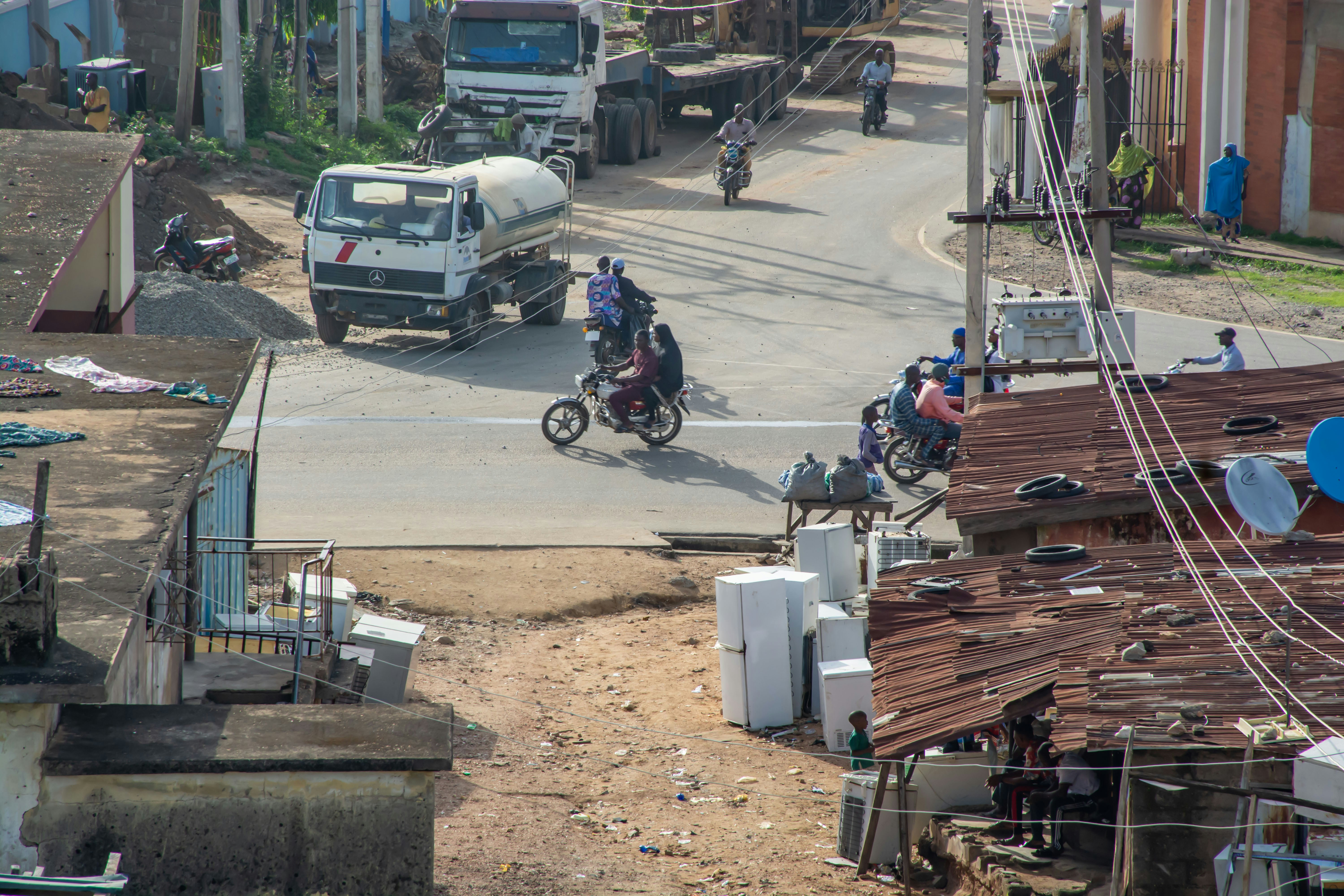 Motorcycles and vehicles converge at a busy junction surrounded by rustic buildings and utility poles.
