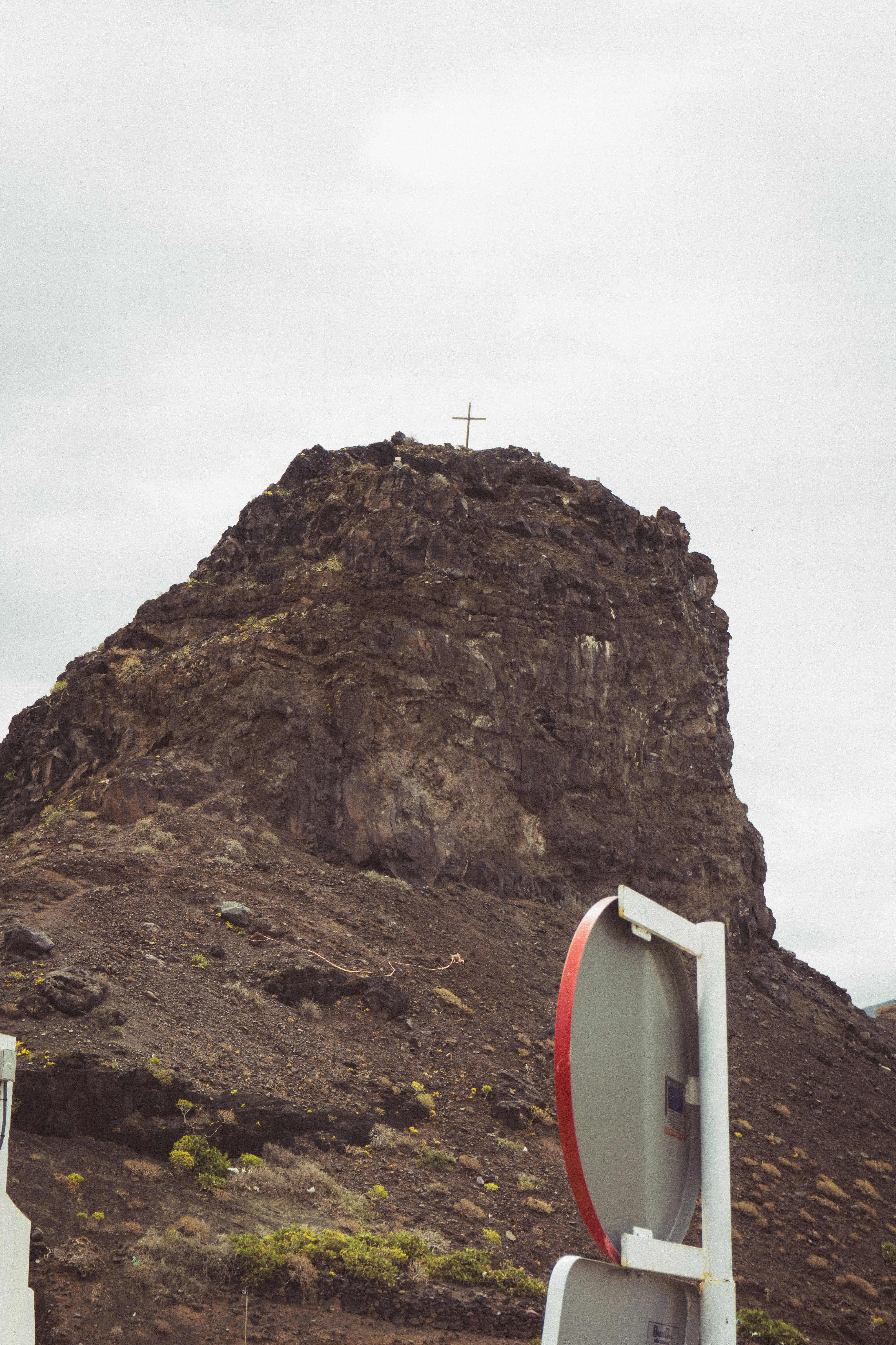 Cross atop a rugged peak above a roadside scene