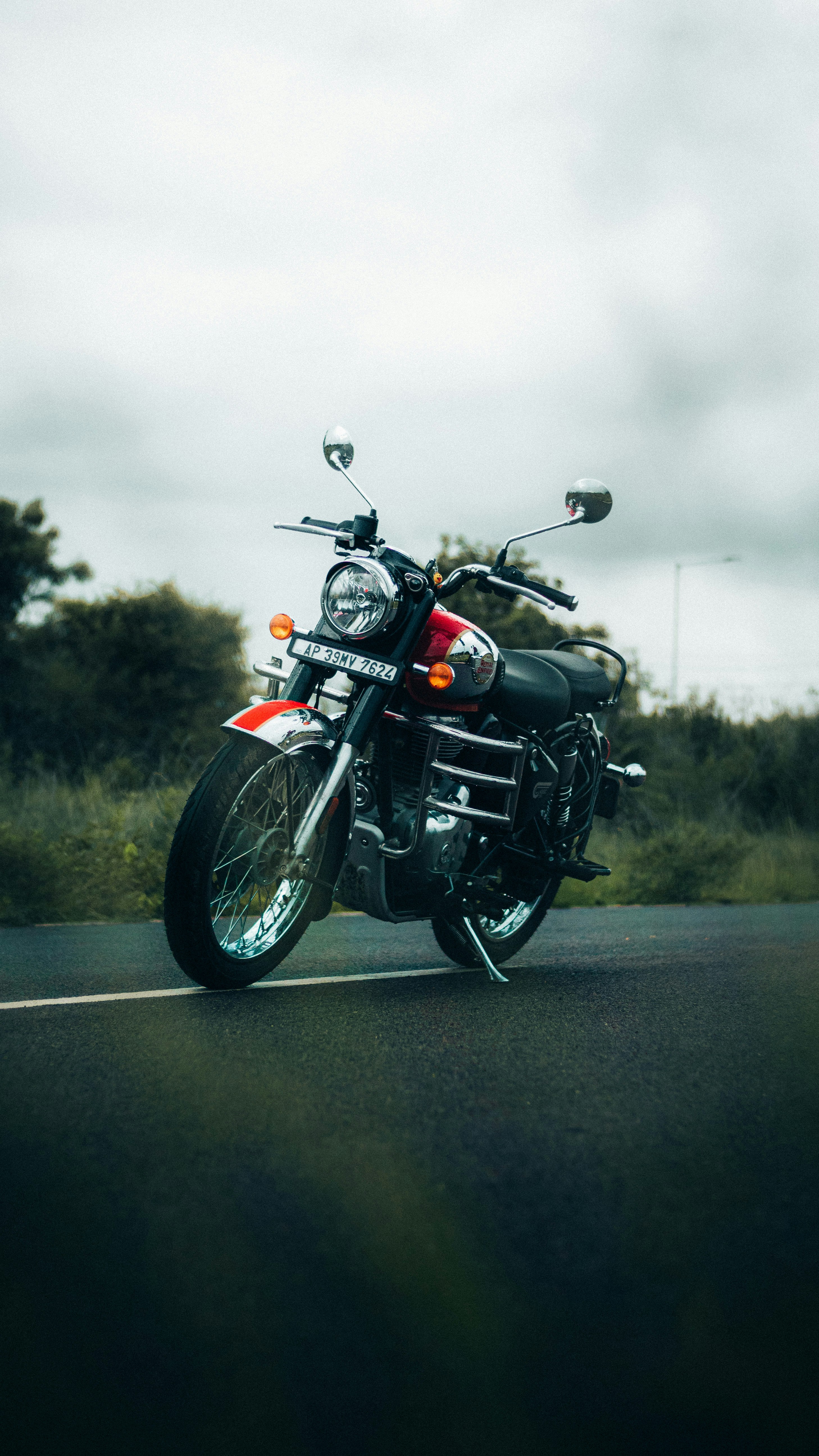 Classic motorcycle parked on a quiet road, surrounded by lush greenery under a cloudy sky.