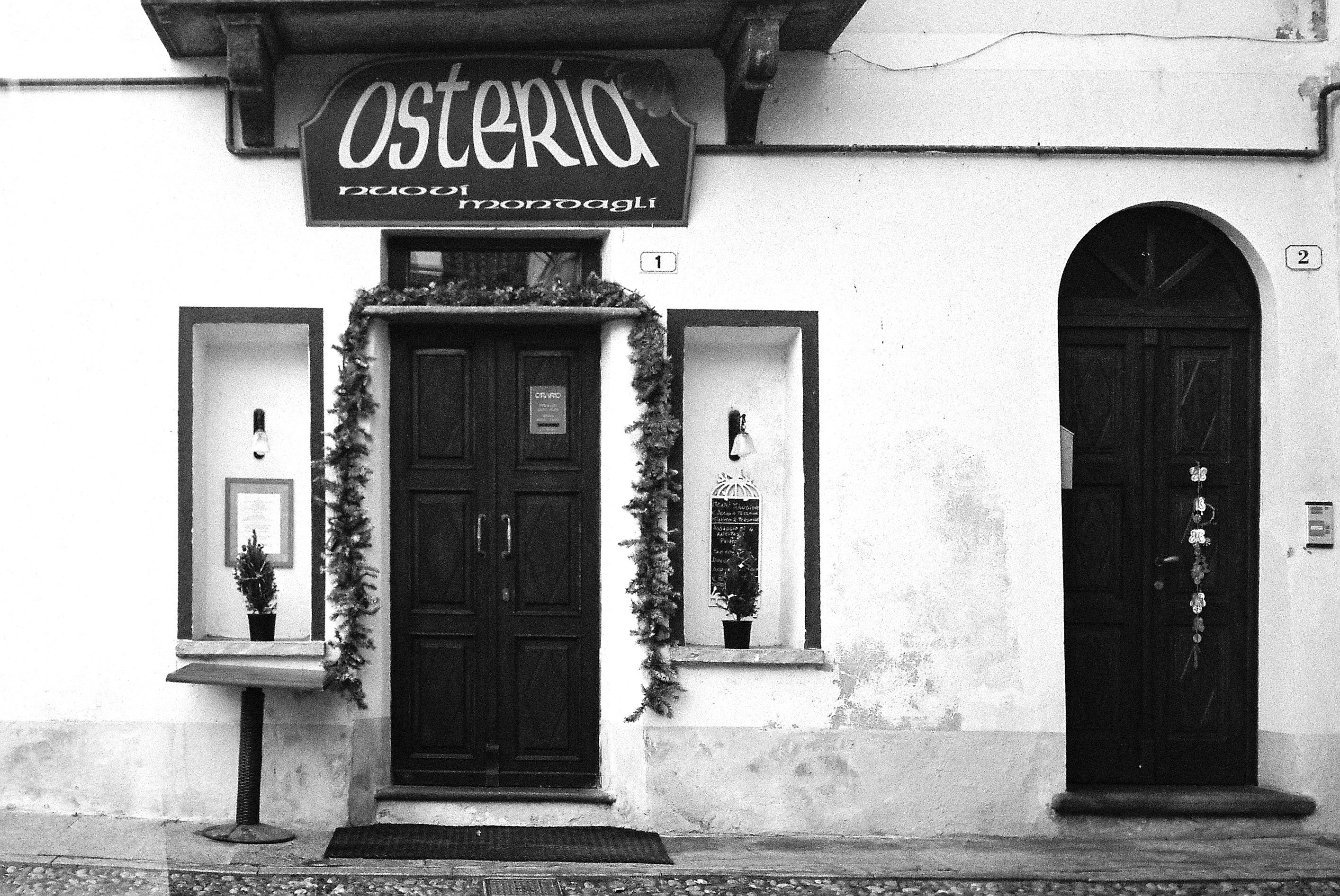 Black and white photo of an osteria entrance with decorative elements on either side.