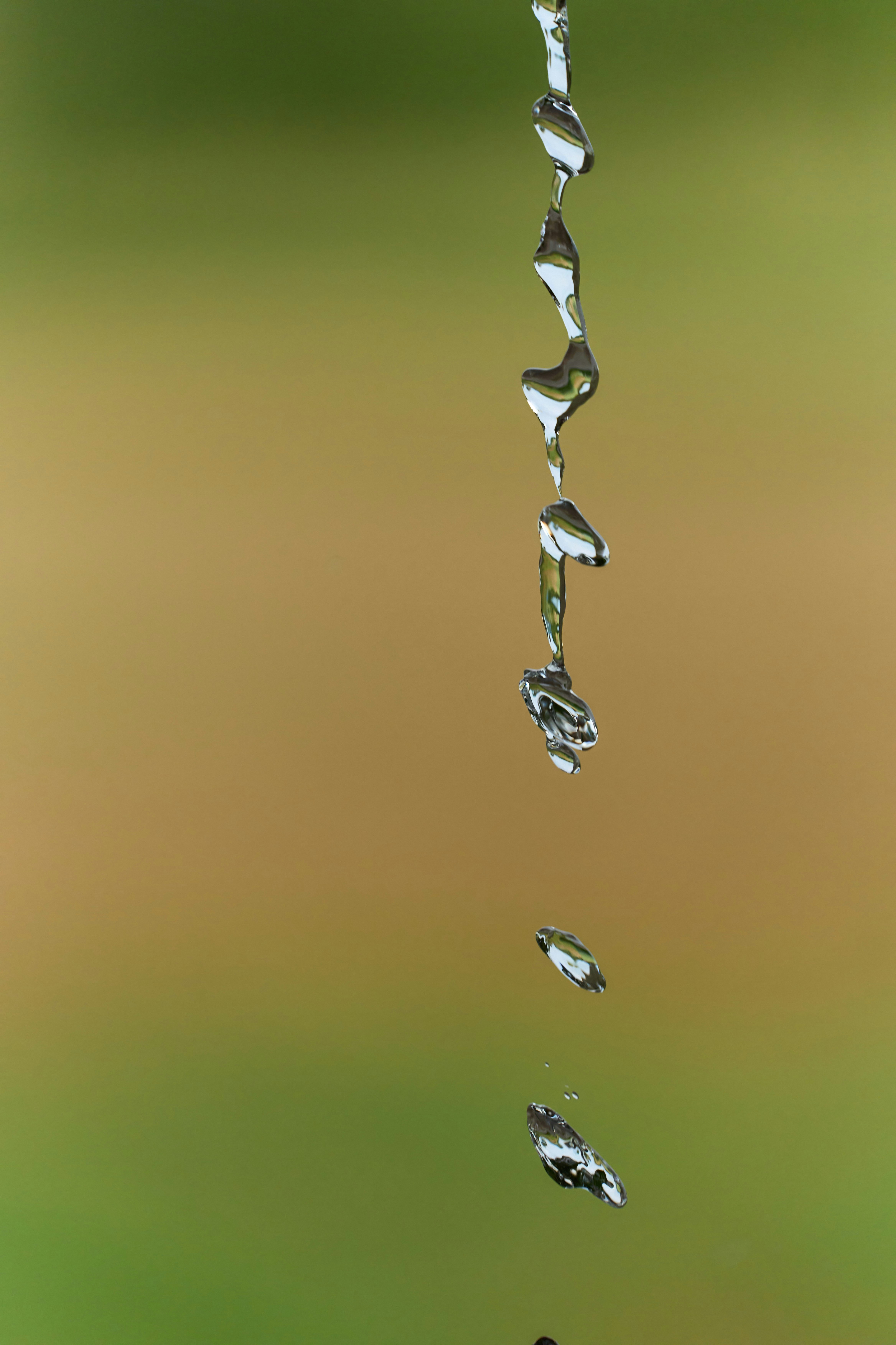 Clear water droplets cascading down against a blurred green background, showcasing the beauty of fluid dynamics.