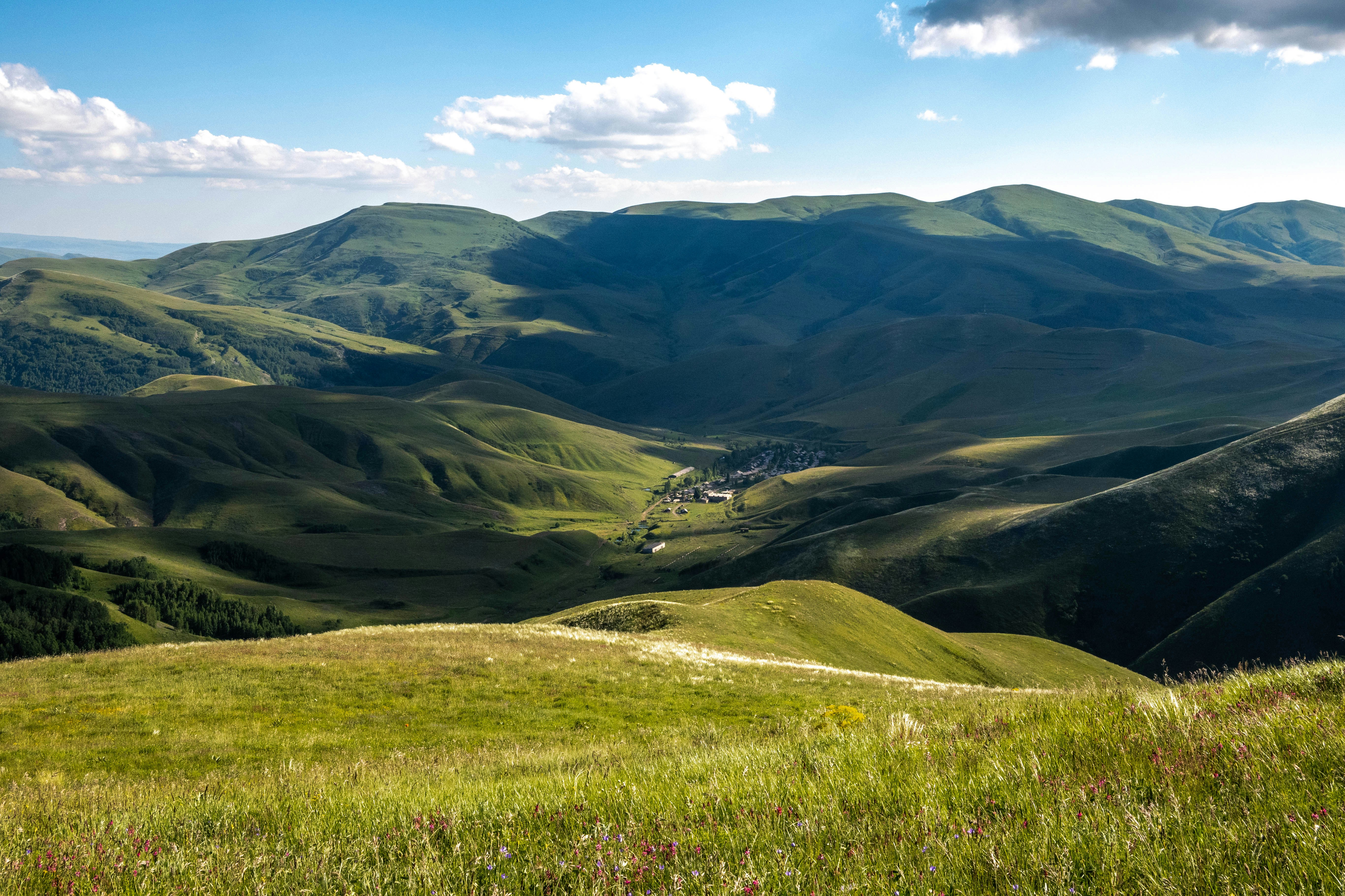 Expansive green valleys and rolling hills under a clear blue sky with scattered clouds.