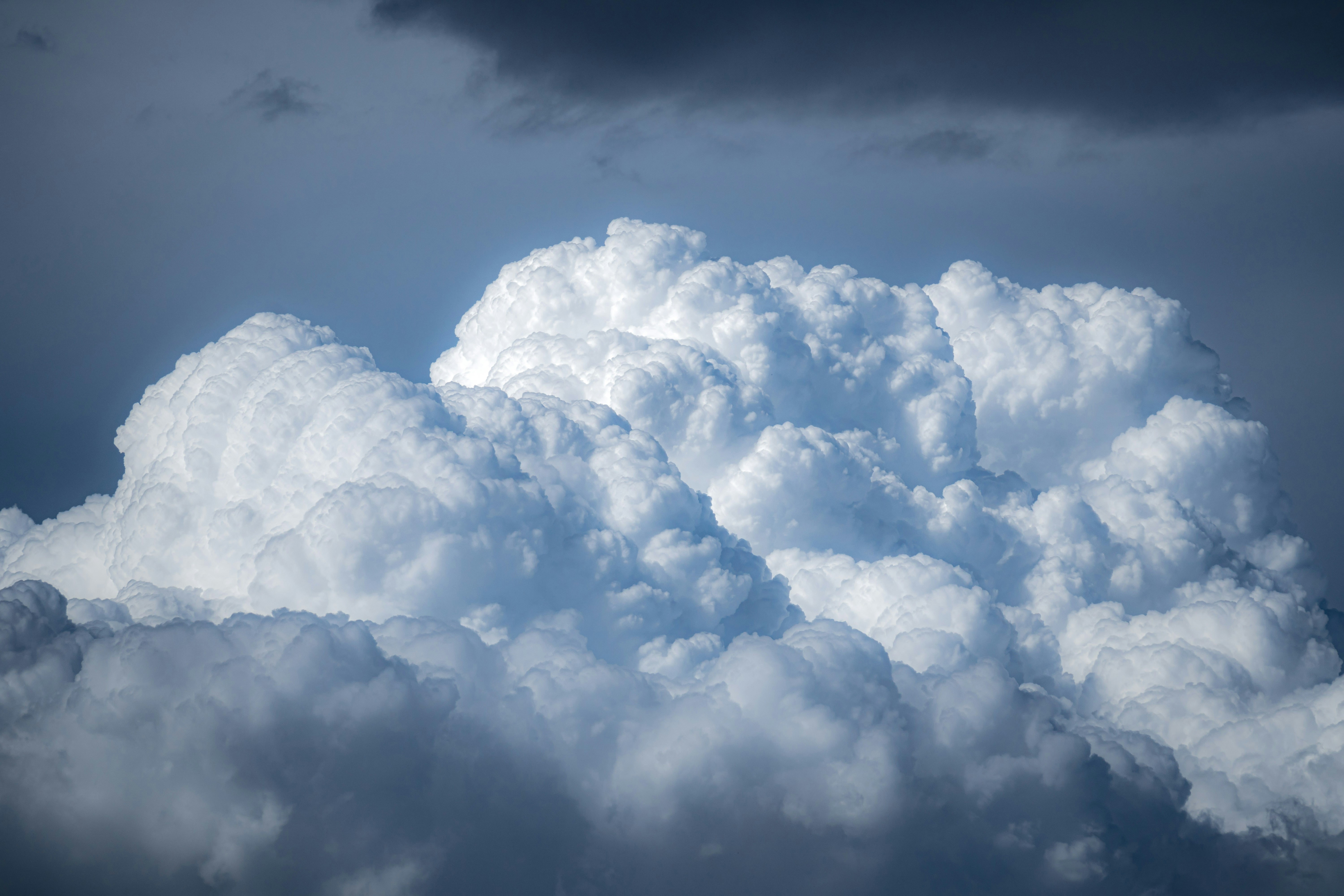 Fluffy white clouds billowing against a backdrop of moody blue skies, showcasing the dynamic interplay of light and shadow.