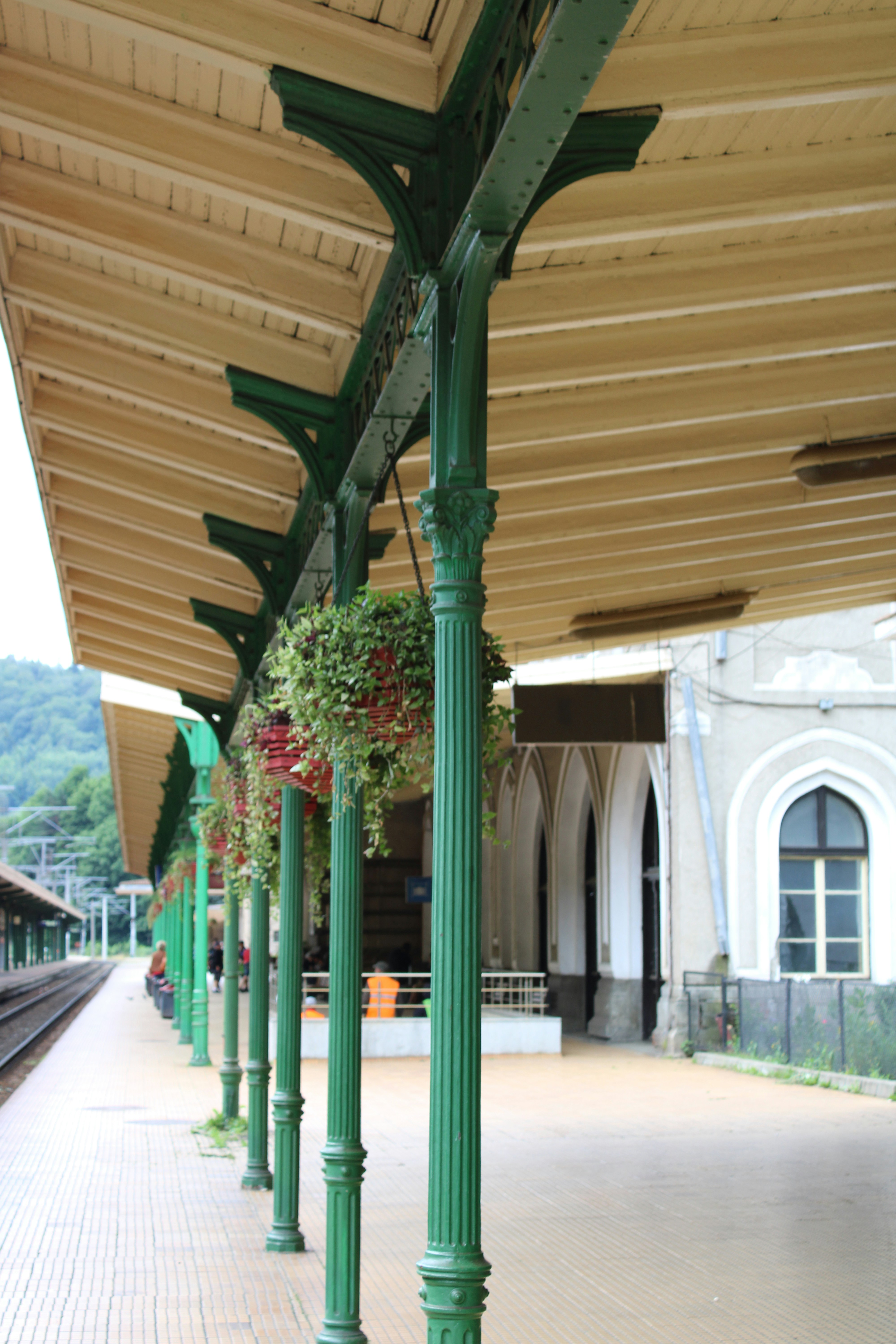 Historic train station platform adorned with green columns and hanging flower baskets, showcasing intricate architectural details.