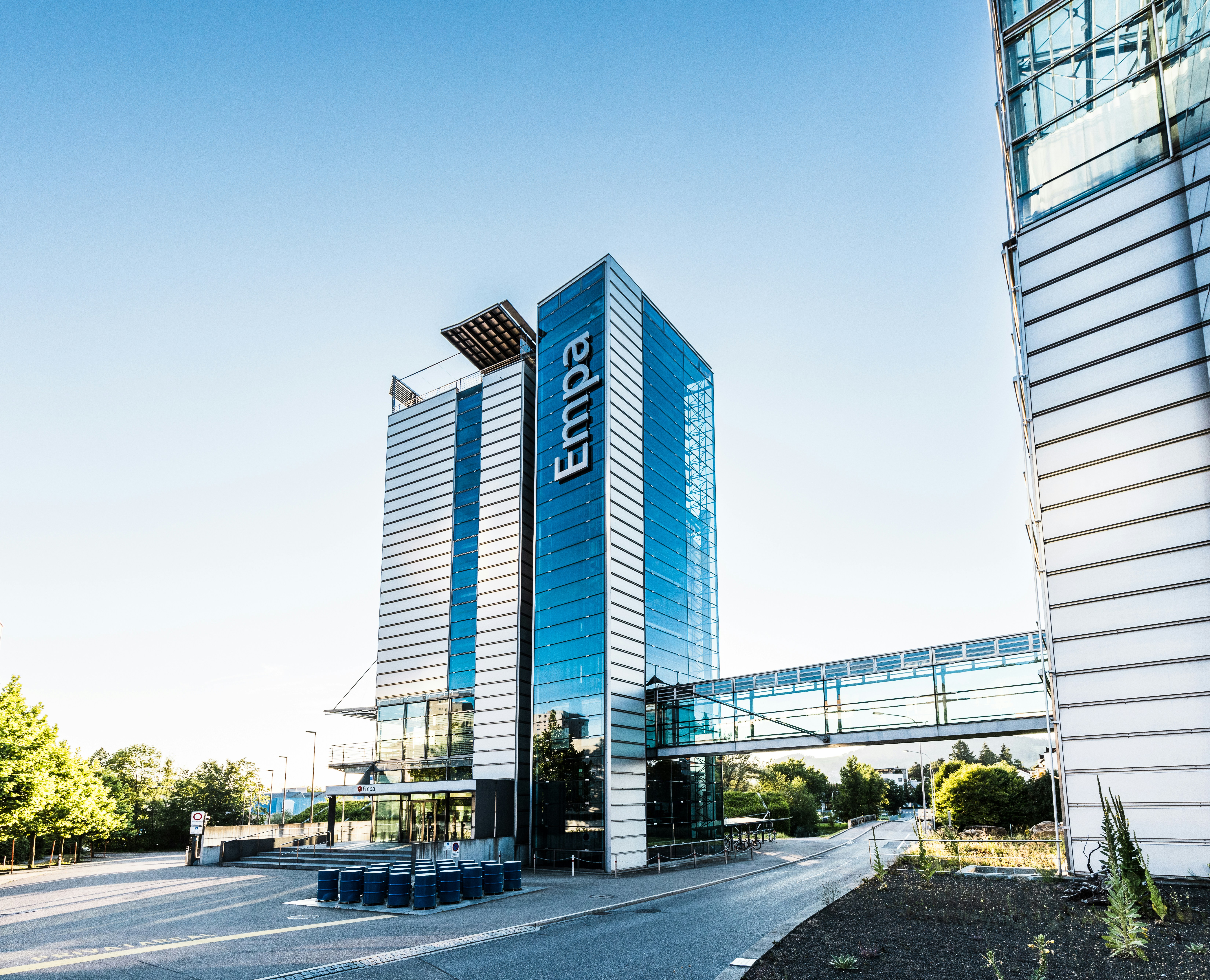 Contemporary glass building with reflective surfaces and a connecting skybridge under a clear blue sky.
