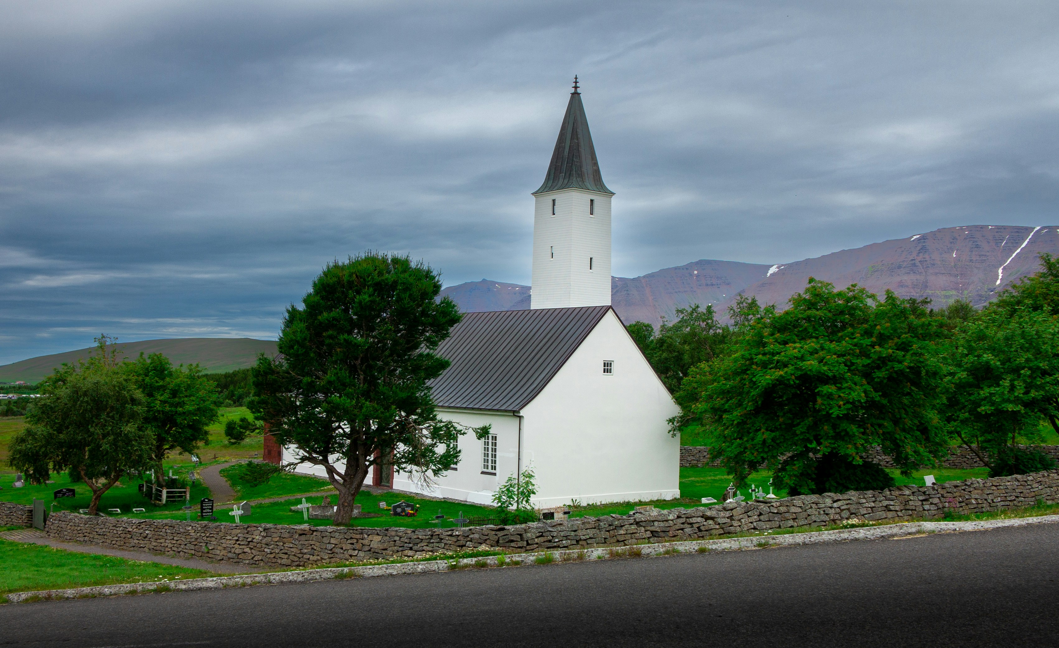 Steeple of Silence: A White Church Against Green Fields and Distant Peaks