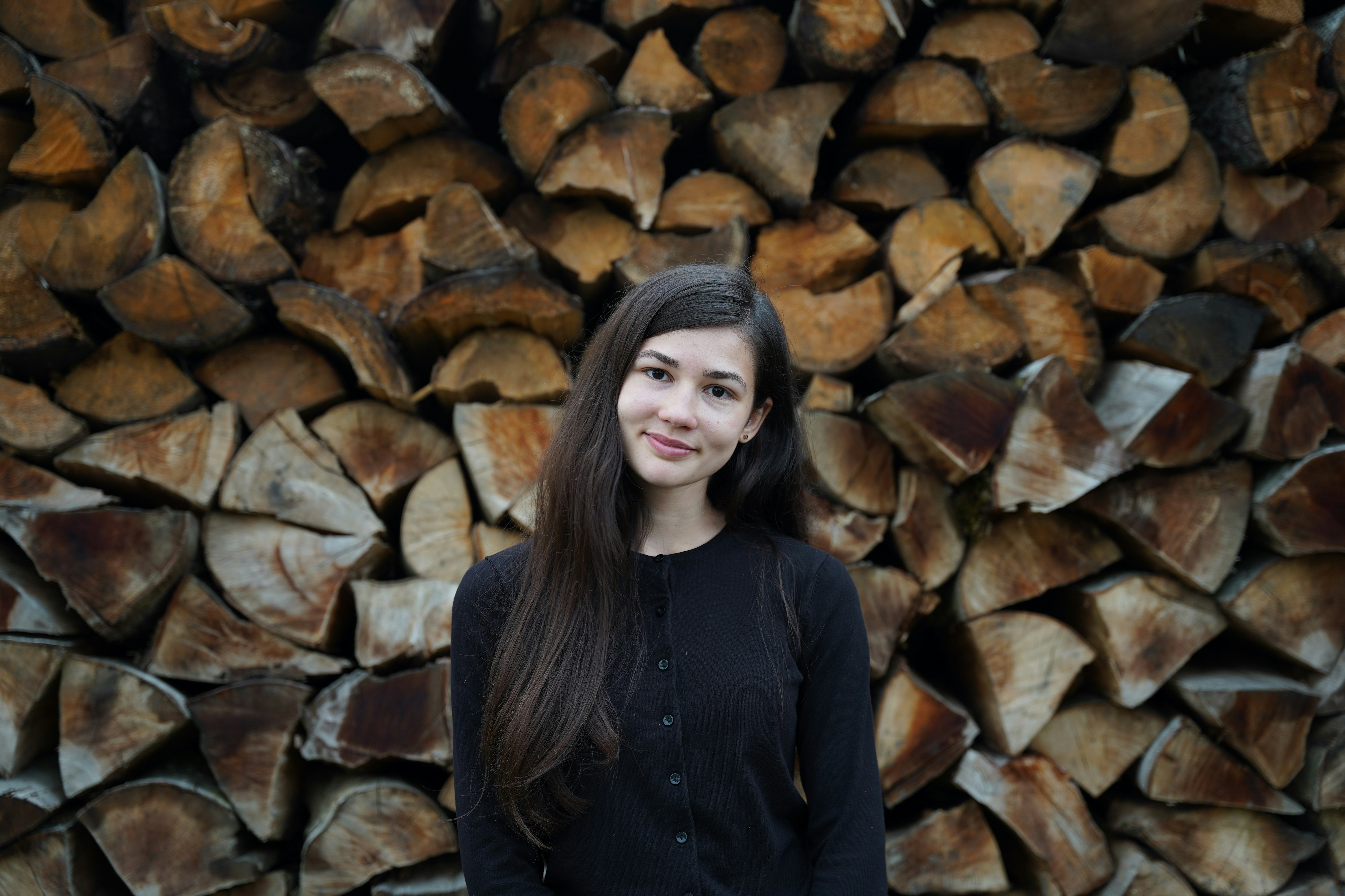 Portrait in the Woodpile: Quiet Confidence Before a Stack of Firewood