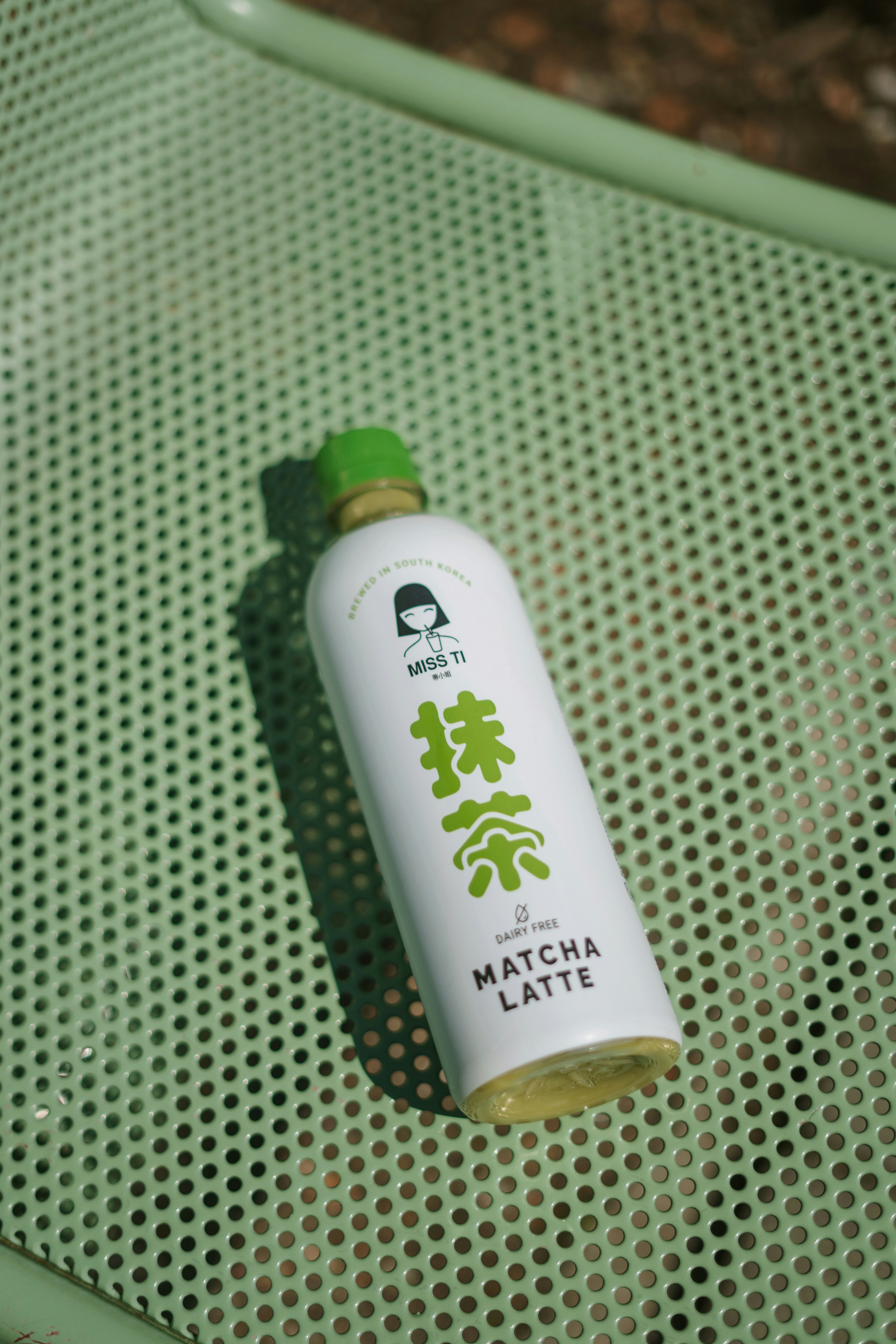 White matcha latte bottle with green label lies diagonally on a perforated mint-green table surface.