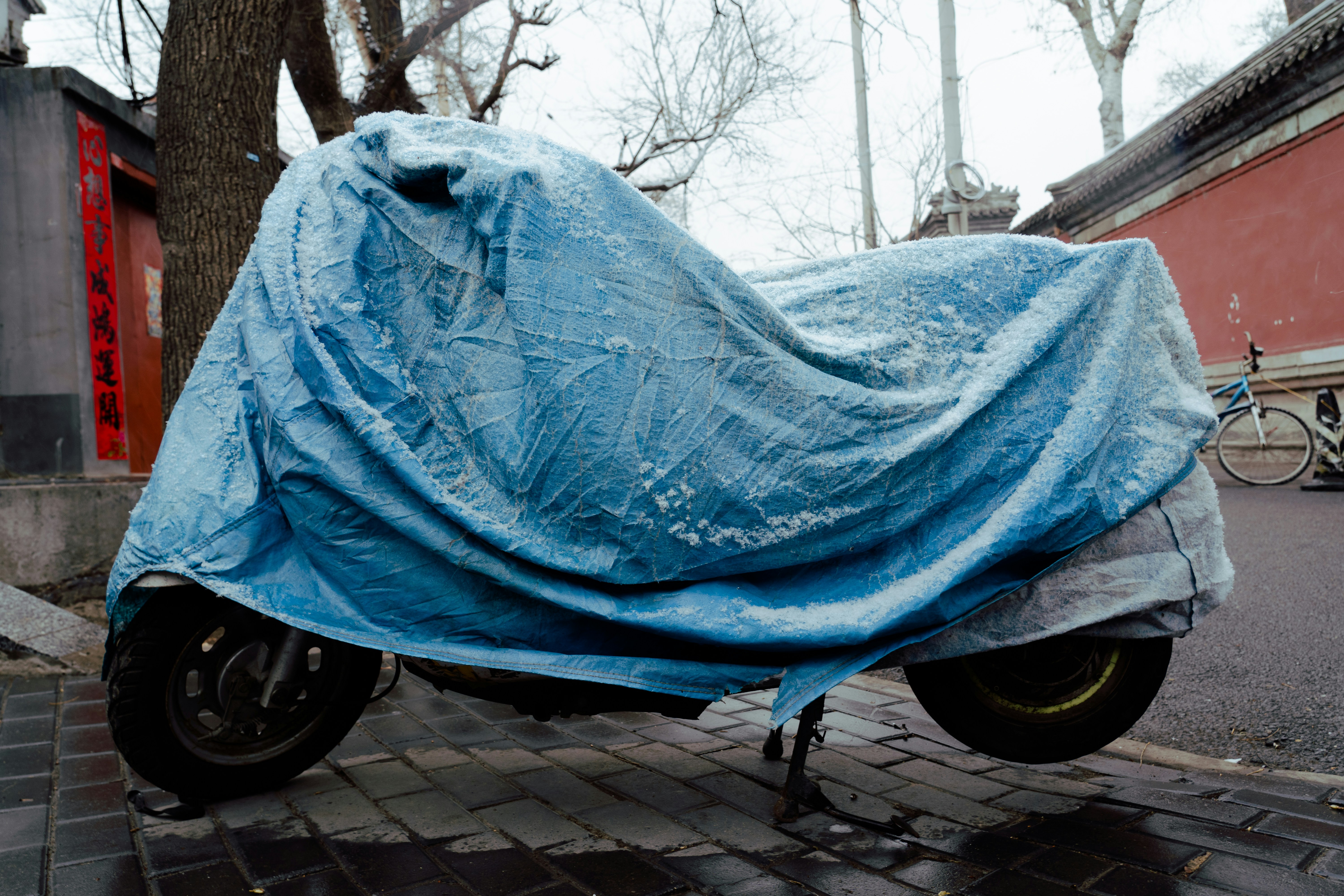 Hidden Muse: A Scooter Veiled in Blue Tarp on a Rainy Street