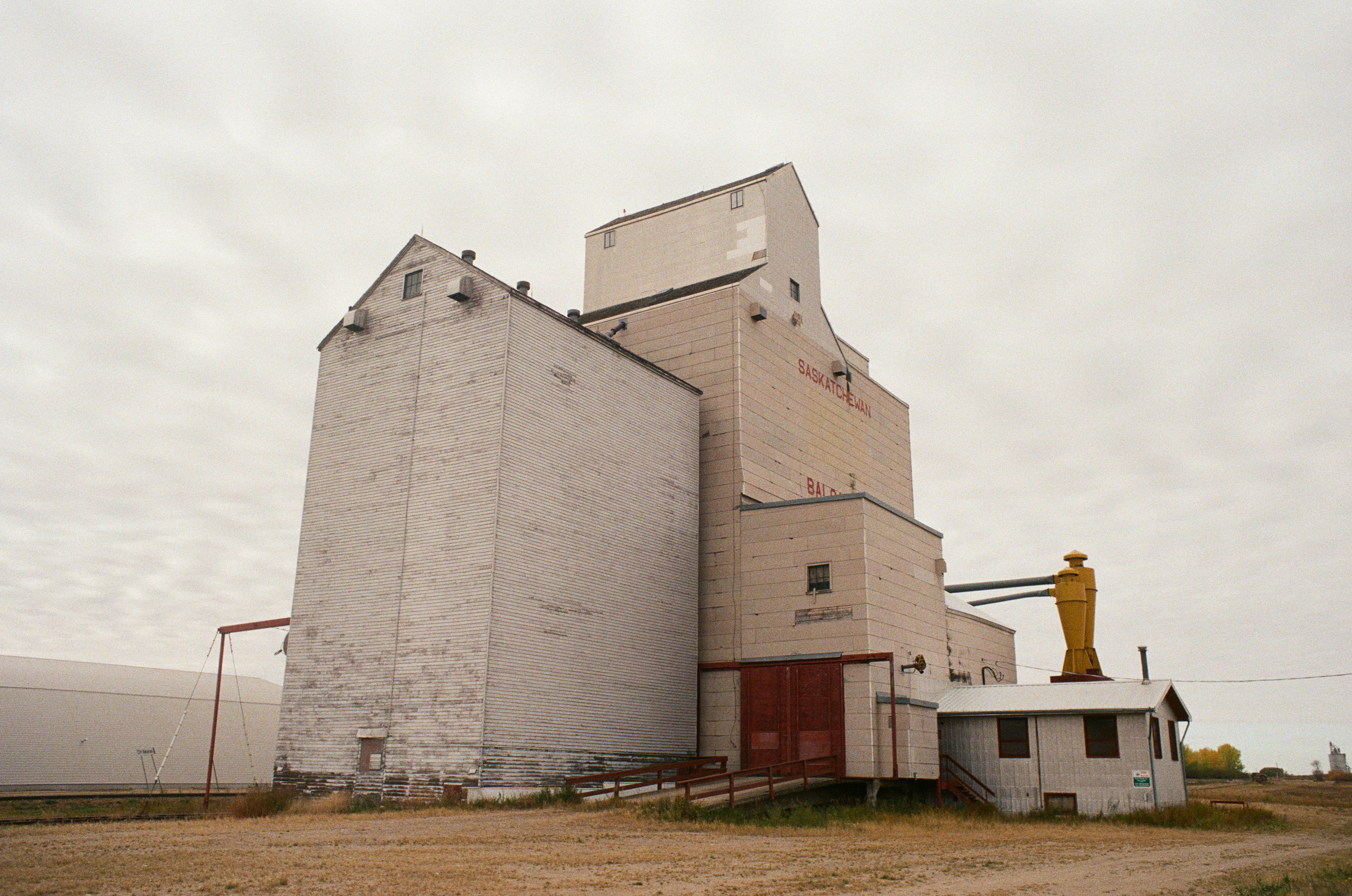 Weathered grain elevator stands tall against a cloudy sky, showcasing its industrial architecture. The structure embodies the essence of rural agriculture.