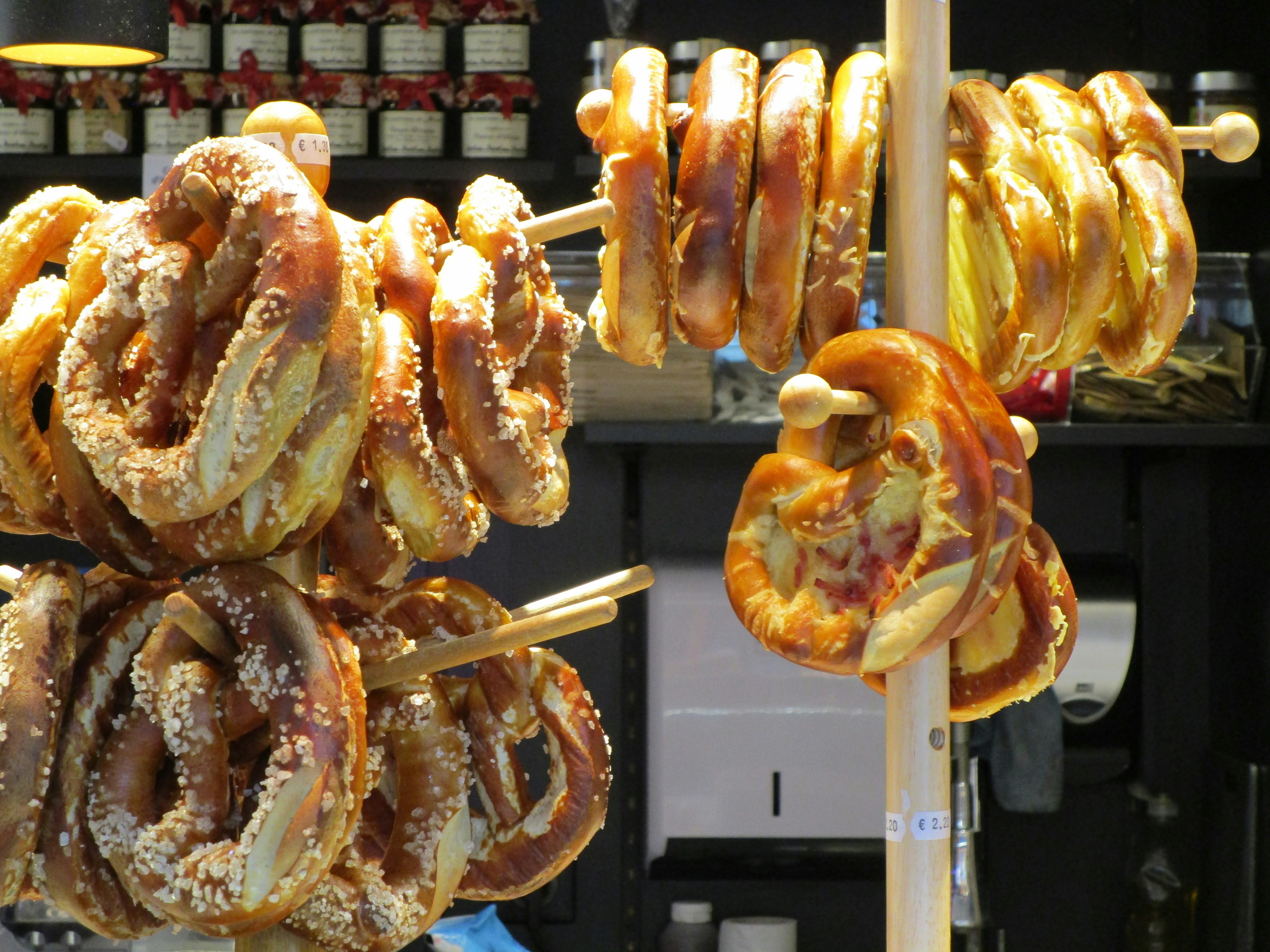 Freshly baked pretzels hang on wooden sticks at an outdoor market stall.