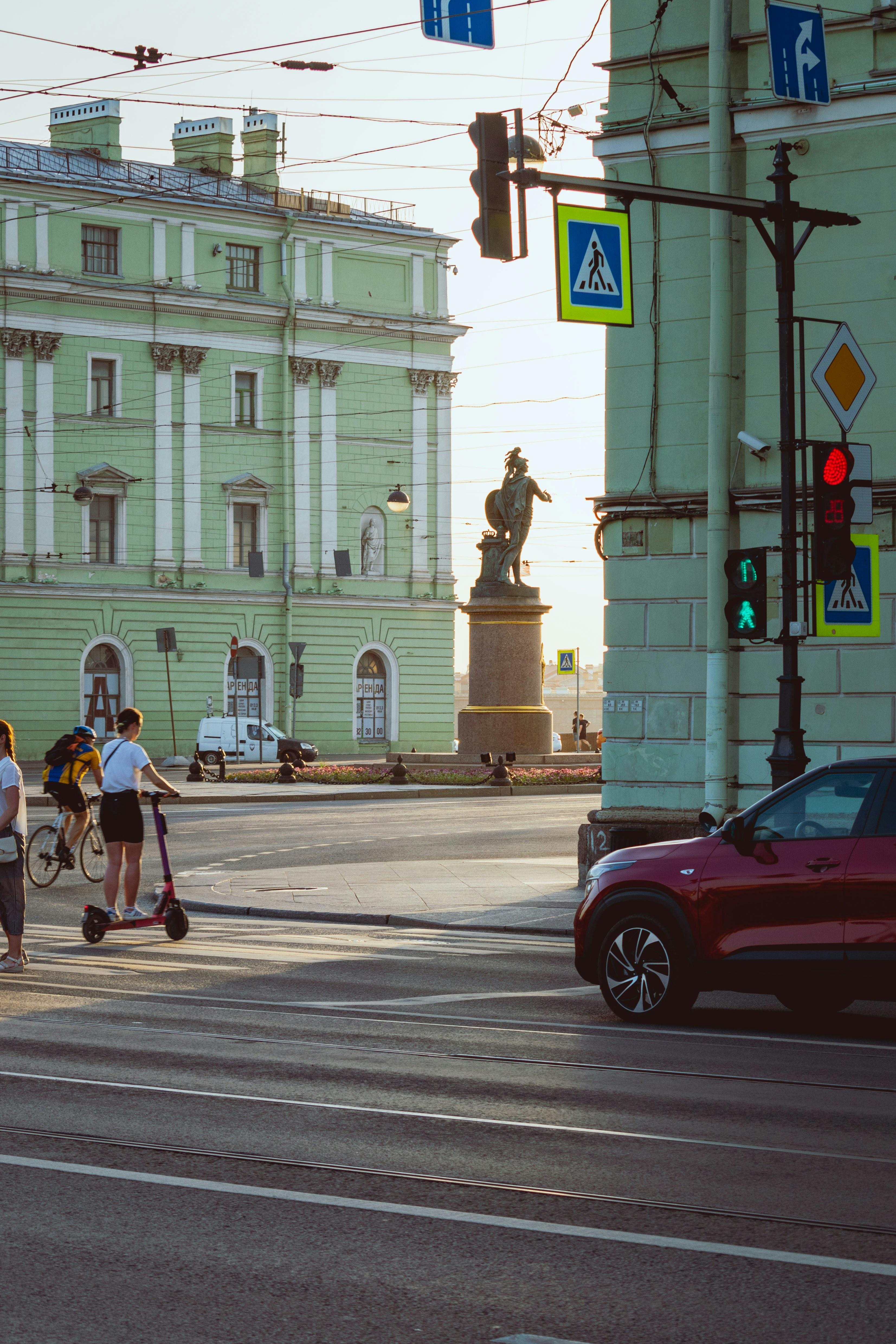 Sunlit Statue at a Busy Intersection Framed by Green Facades