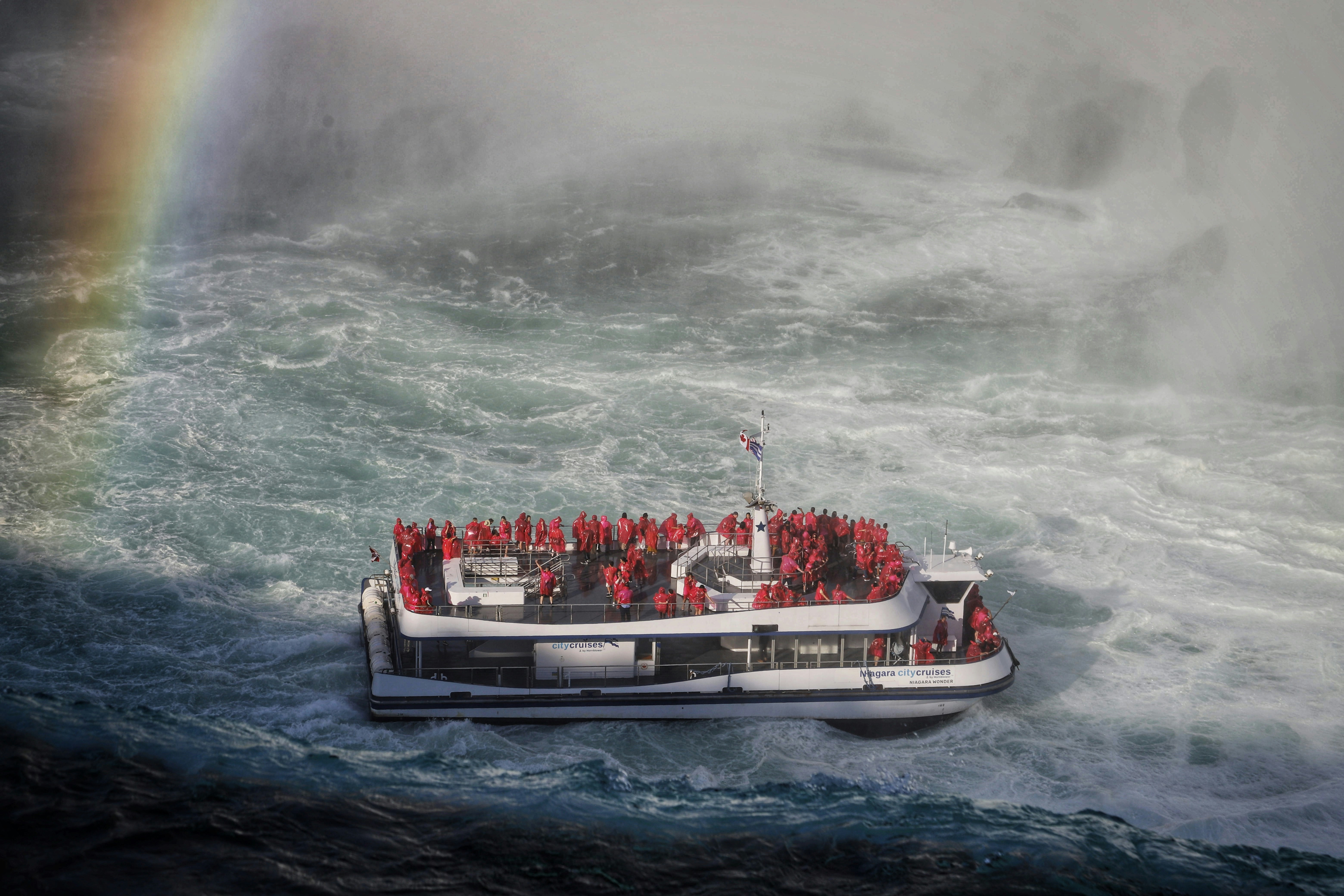 Rainbow over a crowded tour boat slicing through misty whitewater