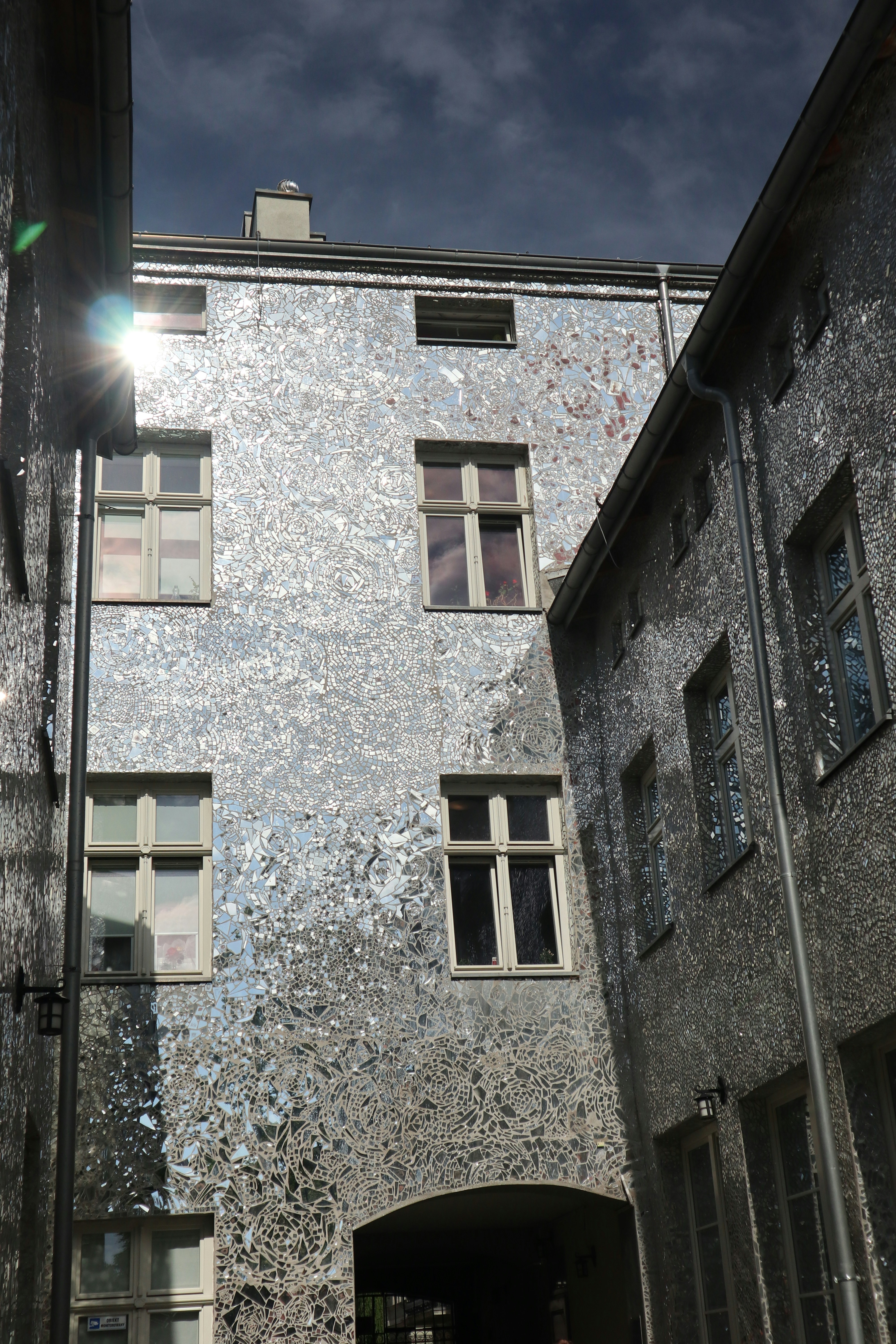 Mirrored Mosaic Courtyard: Sunlit Arch Between Silver Facades