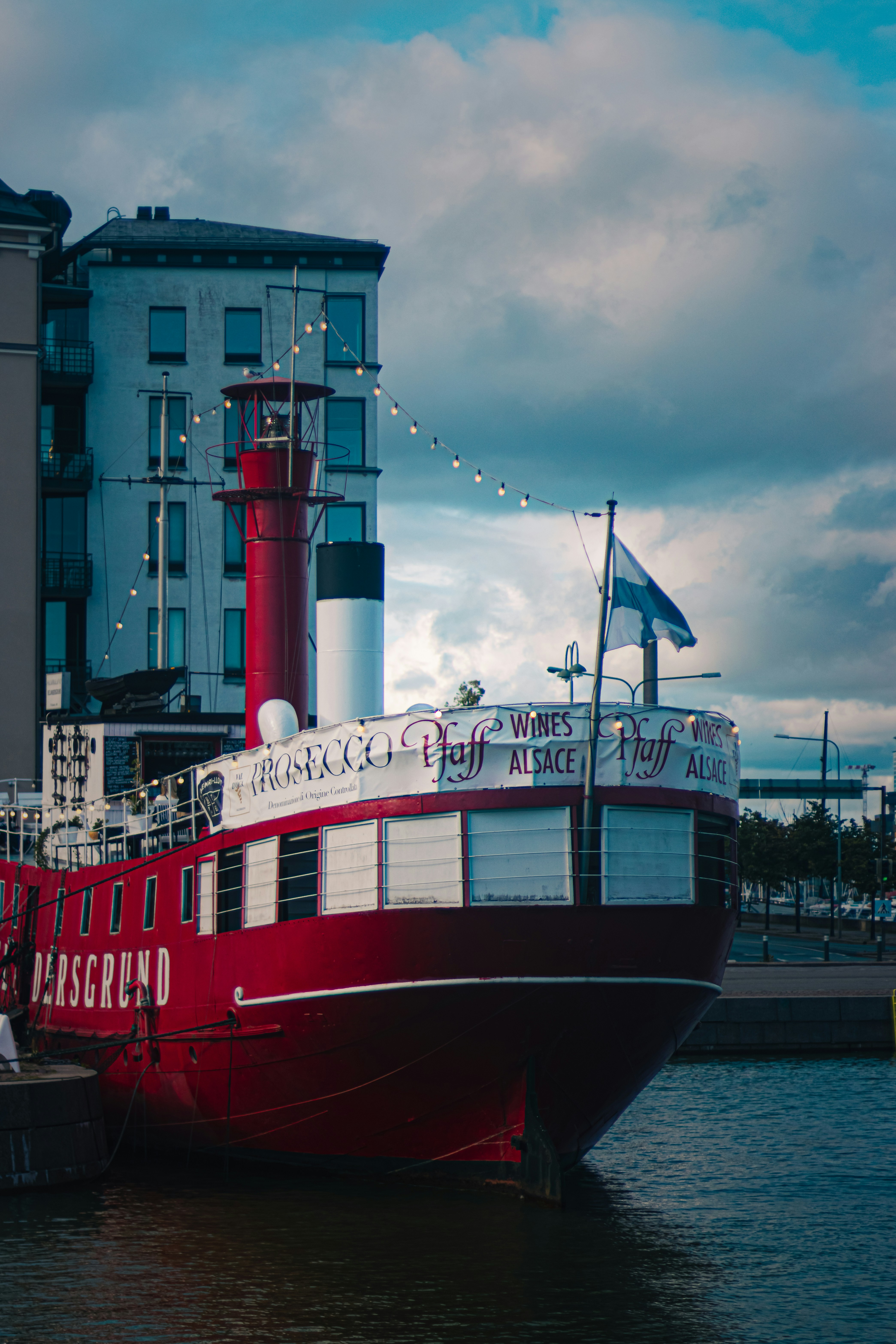 Crimson Riverboat at Dusk: Fairy-Lit Vessel by a Modern Waterfront