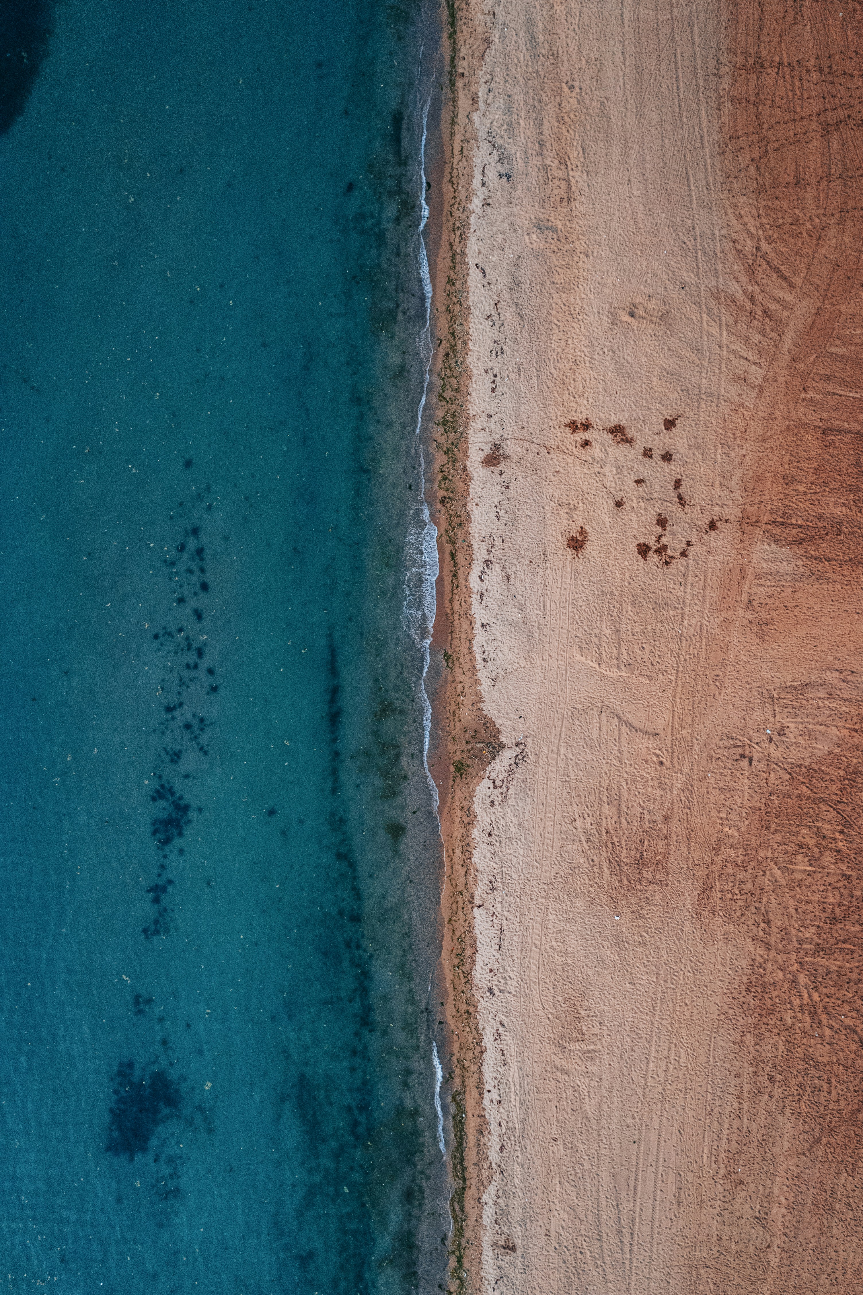 Aerial photograph of a straight shoreline where turquoise water meets pale sand, creating a bold vertical division.