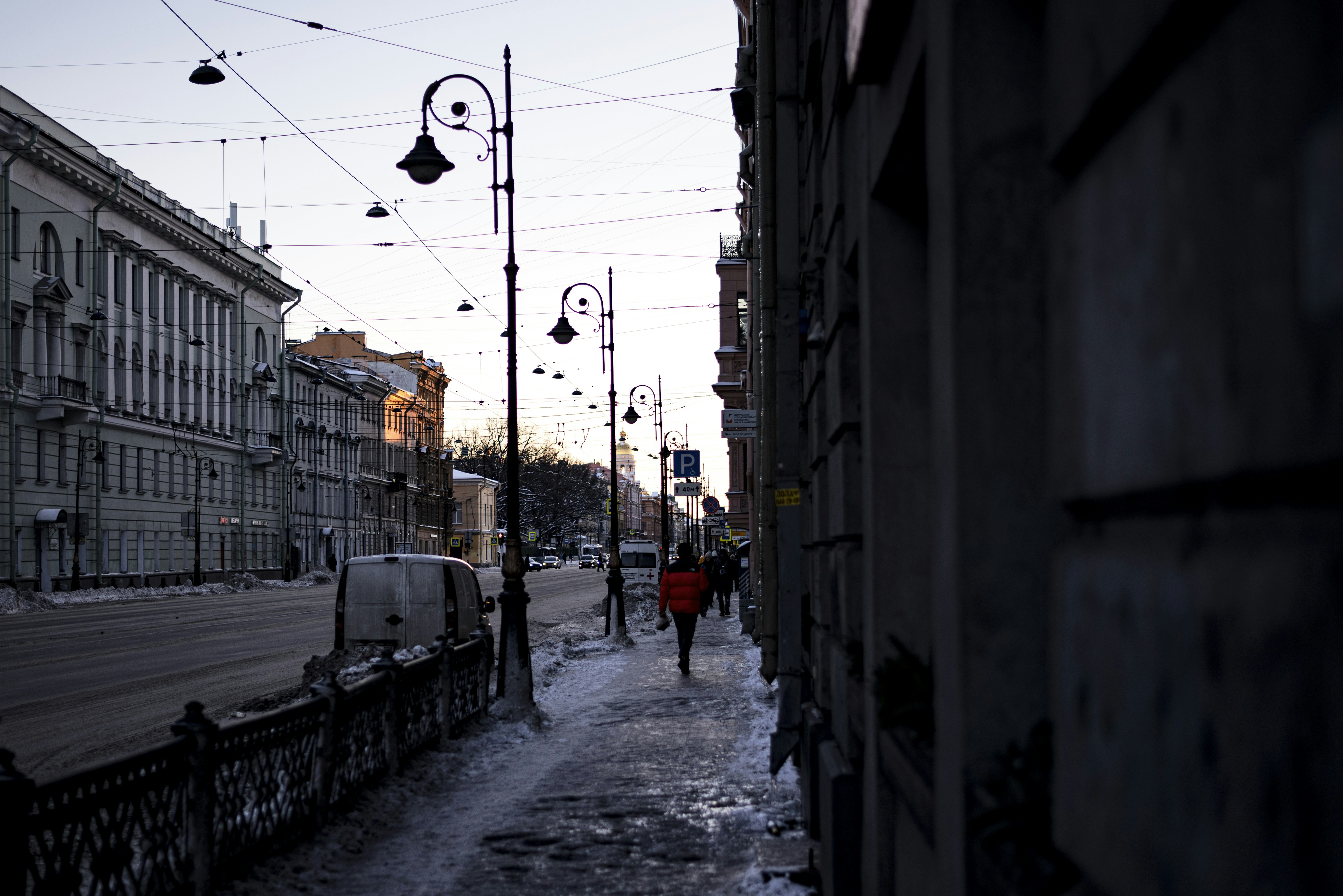 Red-Clad Walkers on a Snow-Cuffed City Street at Dusk Beneath Vintage Lanterns
