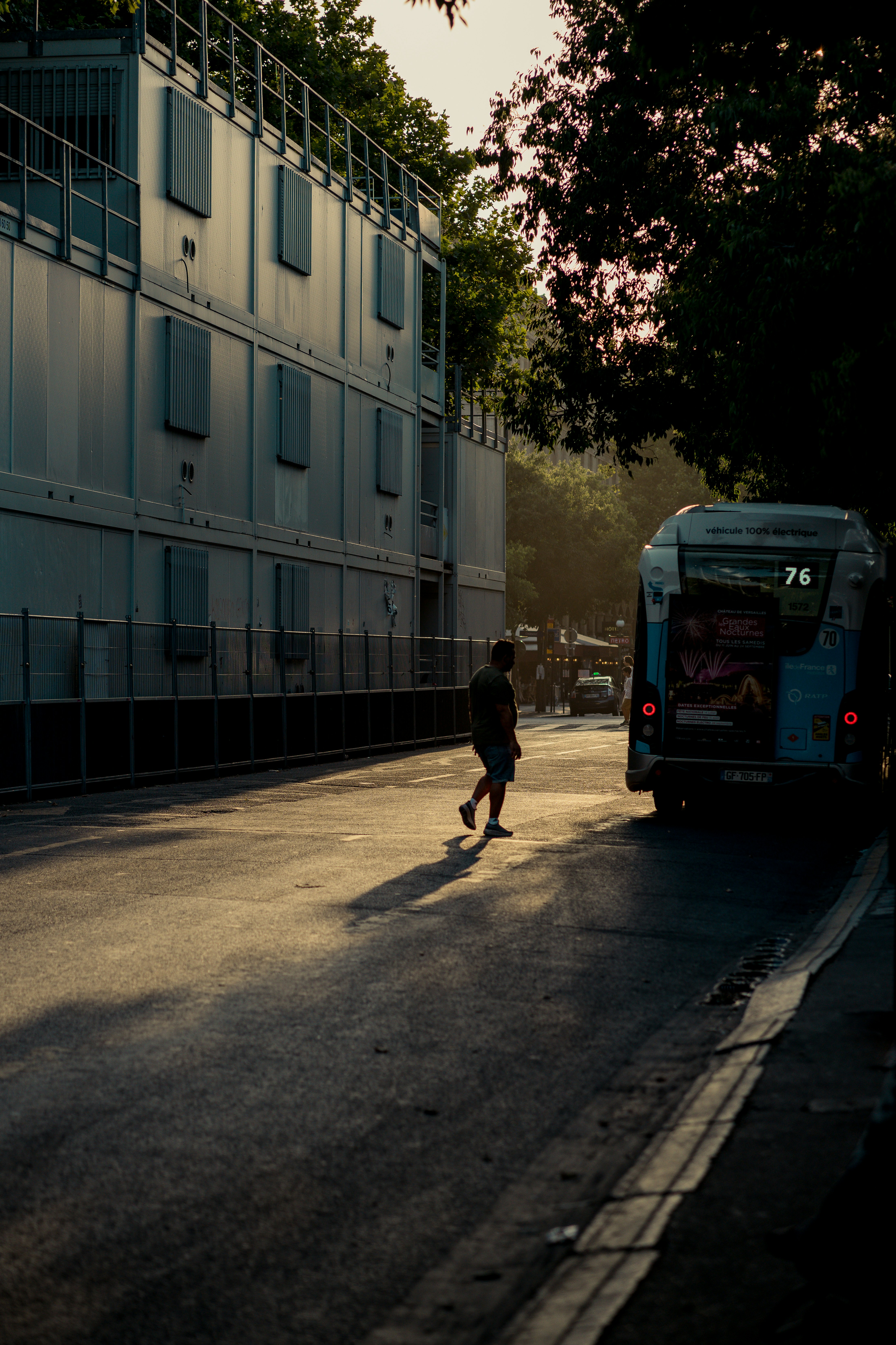 Golden Hour Crossing: A lone pedestrian threads between a modern façade and a waiting city bus