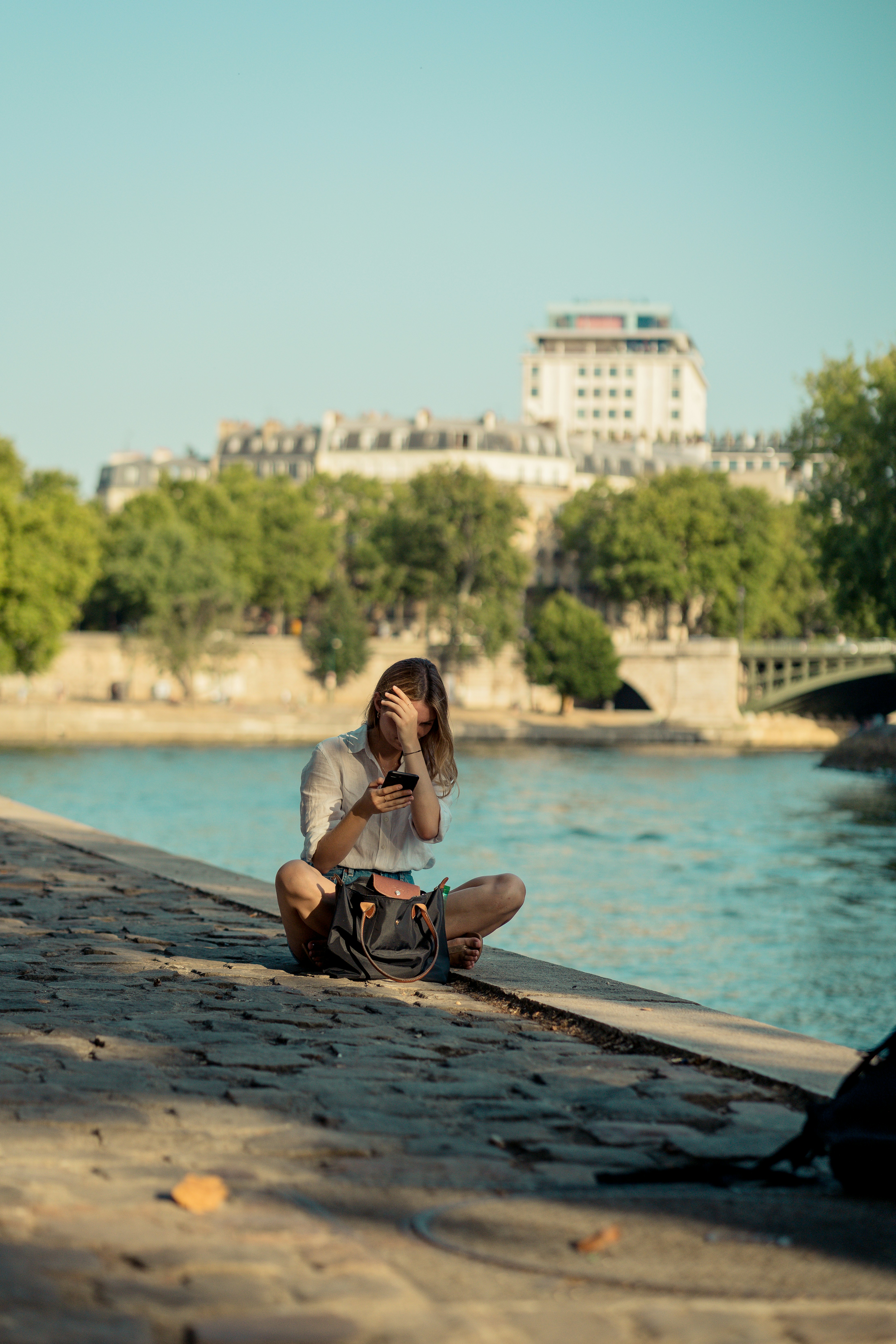 Paused in the Waterfront: A woman with smartphone by the river