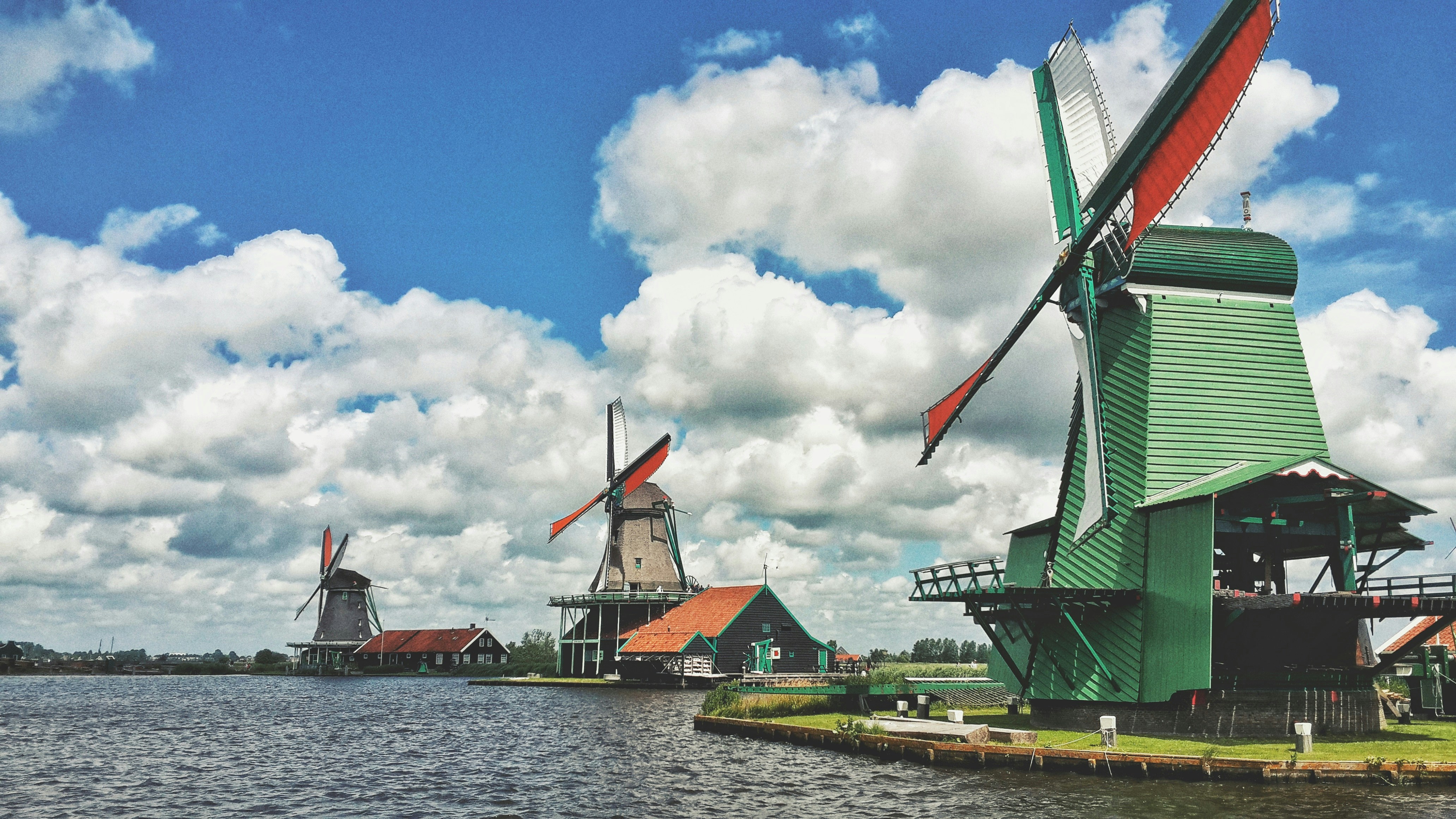 Traditional Dutch windmills stand gracefully along a serene waterway under a dramatic sky. The vibrant colors of the structures contrast beautifully with the clouds above.