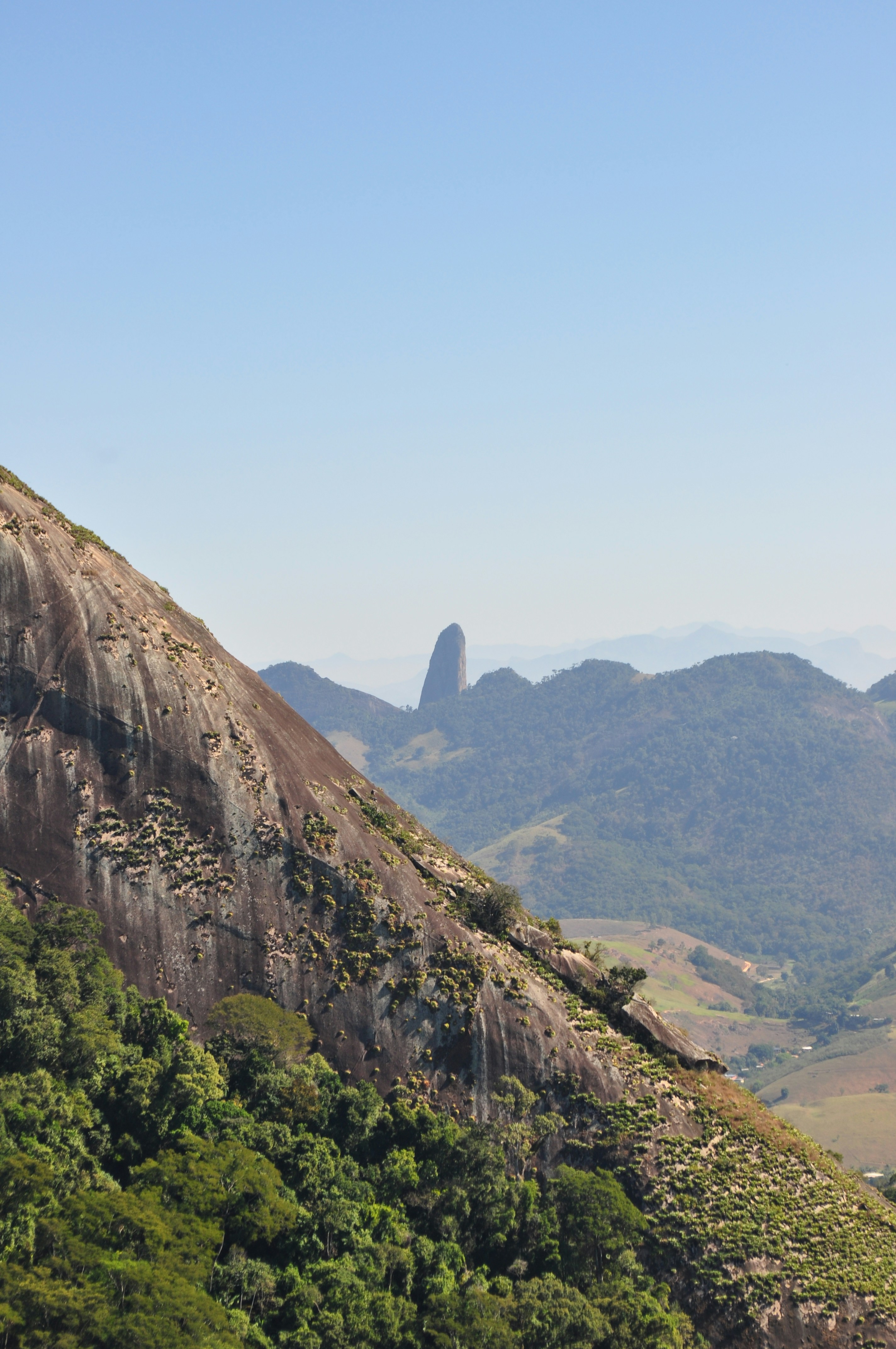 Dramatic mountain landscape with a prominent rocky peak against a clear blue sky.