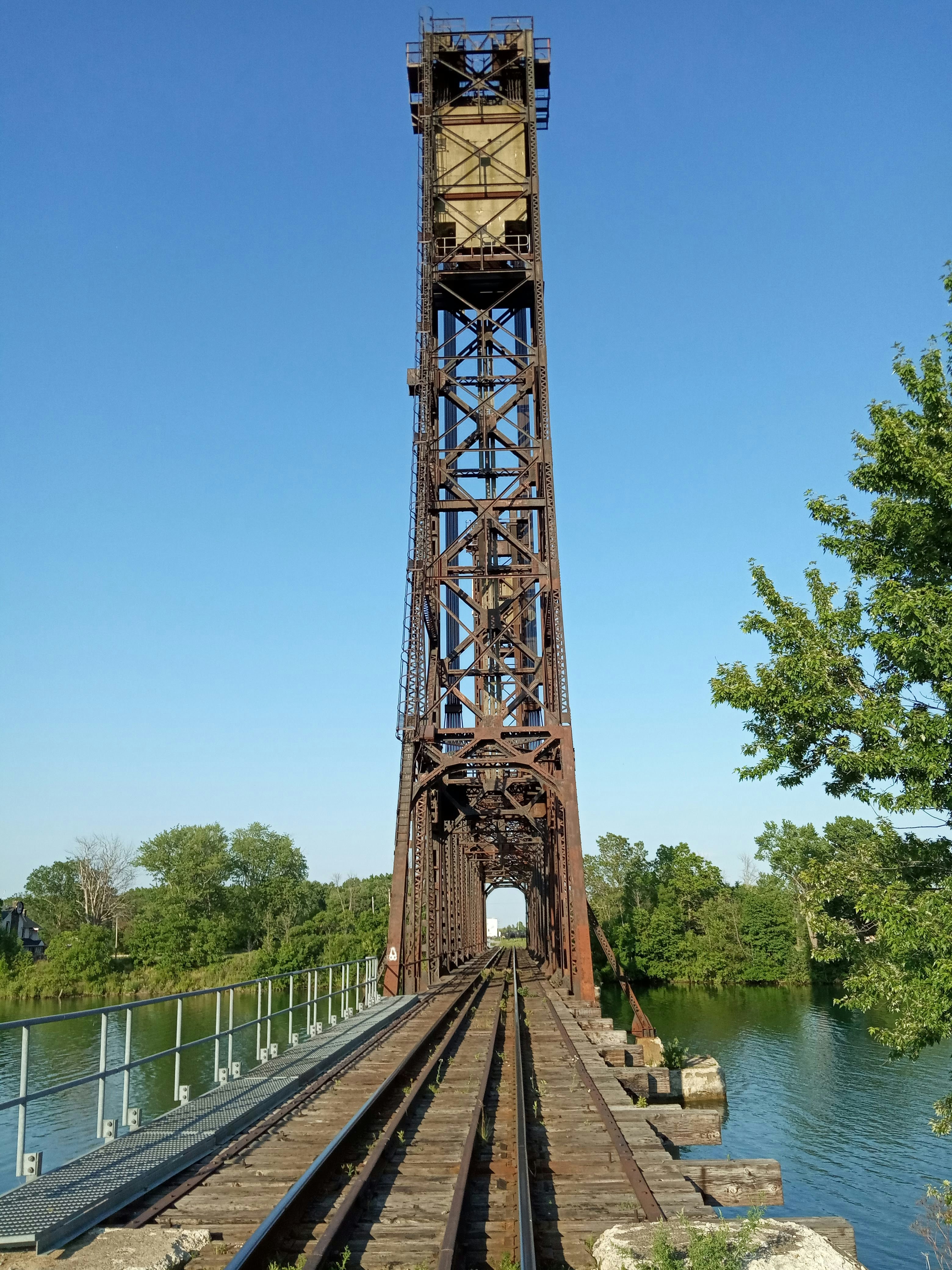 Iron Sentinel Over the River: A Rusted Railway Bridge Reaching for the Sky