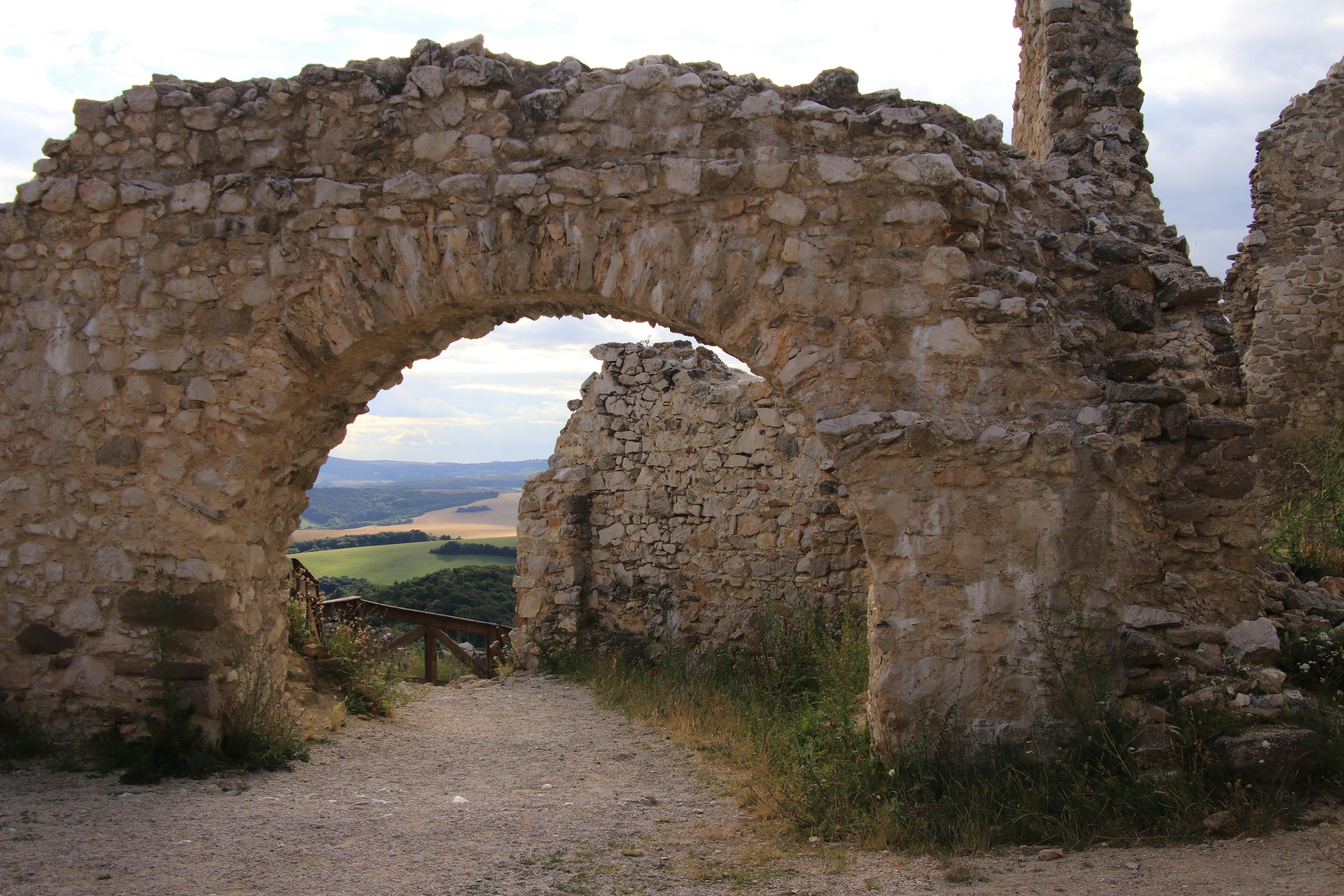 Ruins of an ancient stone archway leading to a lush valley beneath a cloudy sky.