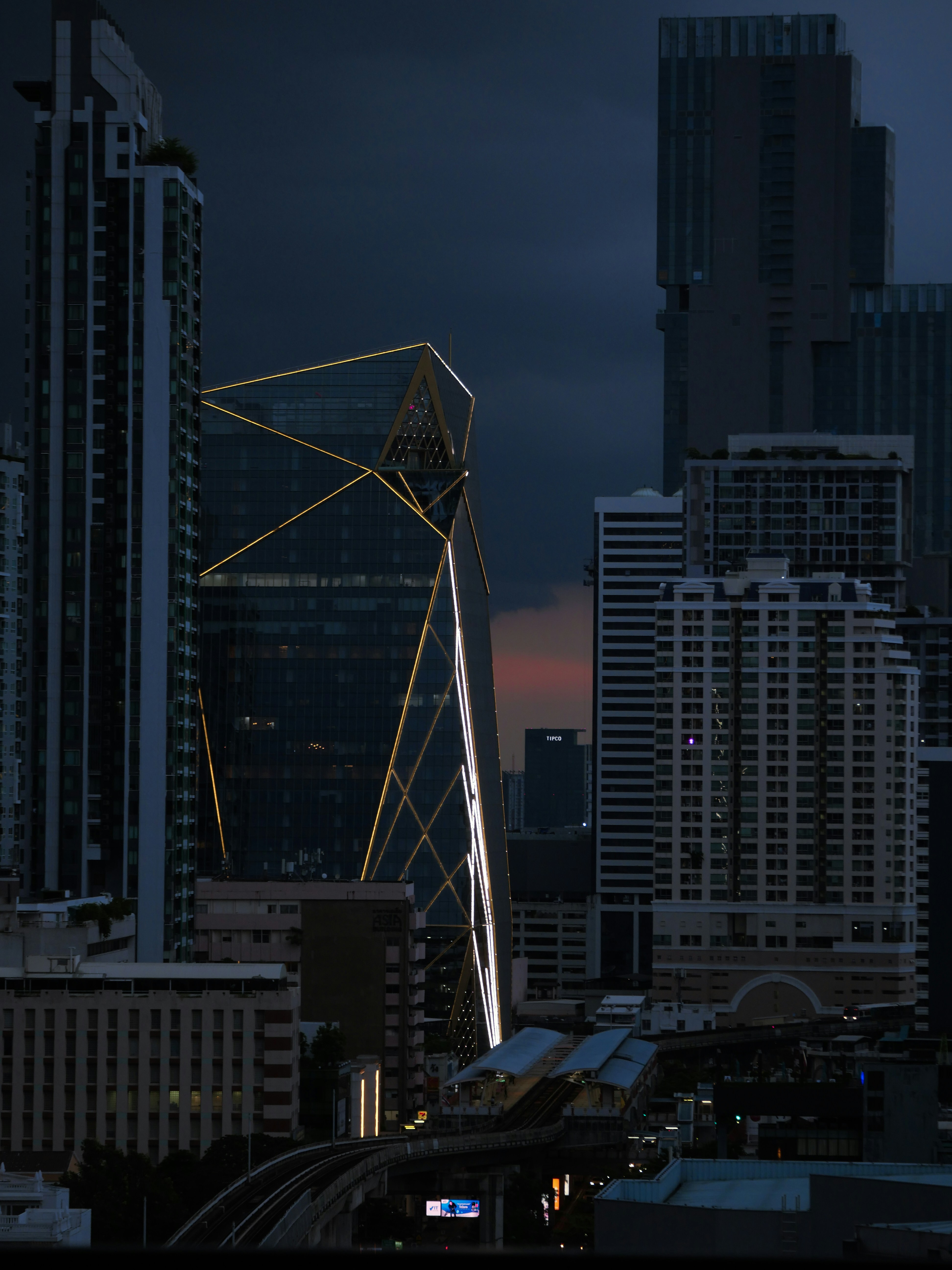 Modern skyscrapers with illuminated geometric designs contrast against a darkening sky, highlighting architectural innovation.