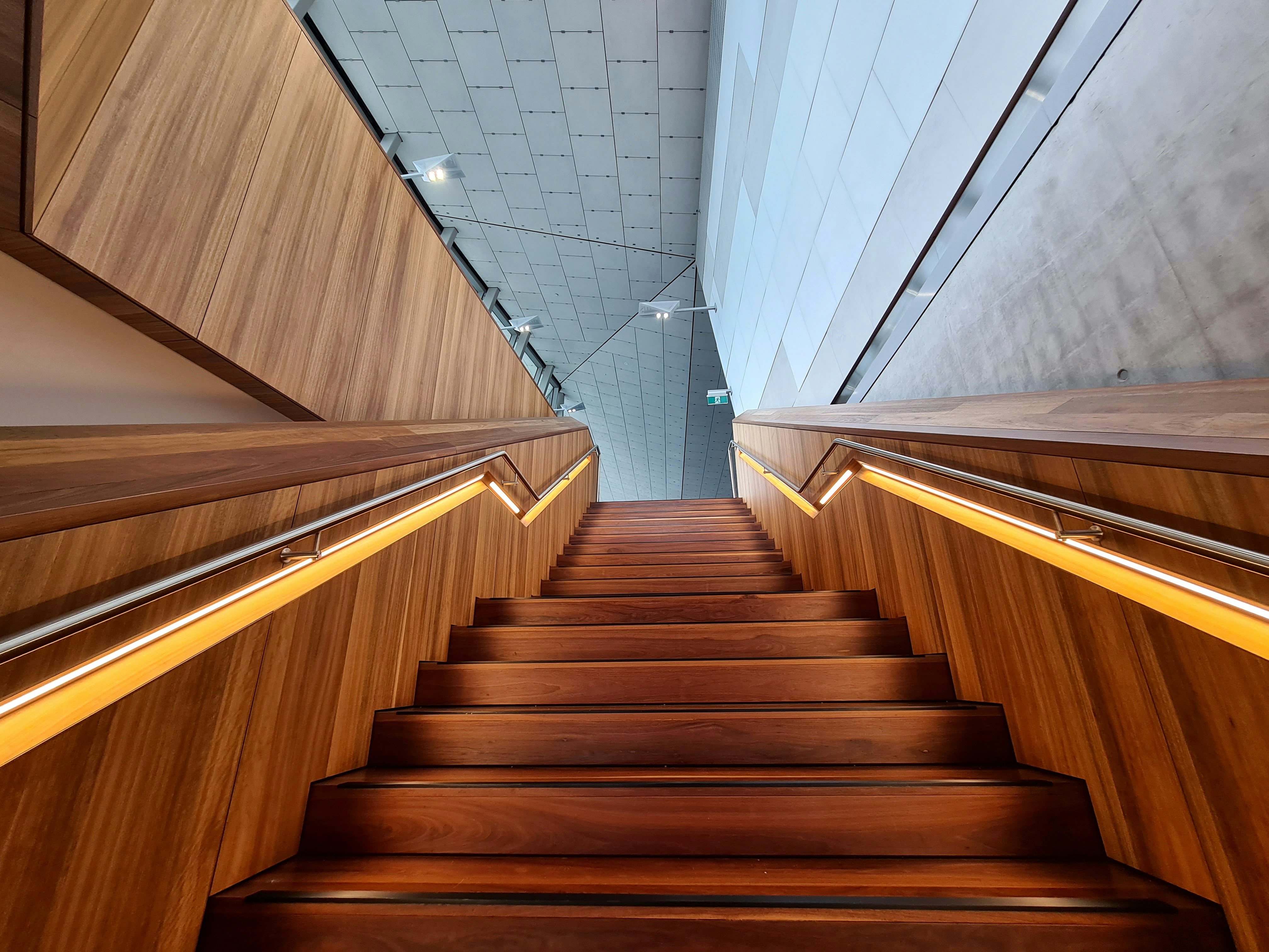 Wooden staircase illuminated by soft lighting, leading upward in a contemporary architectural space.