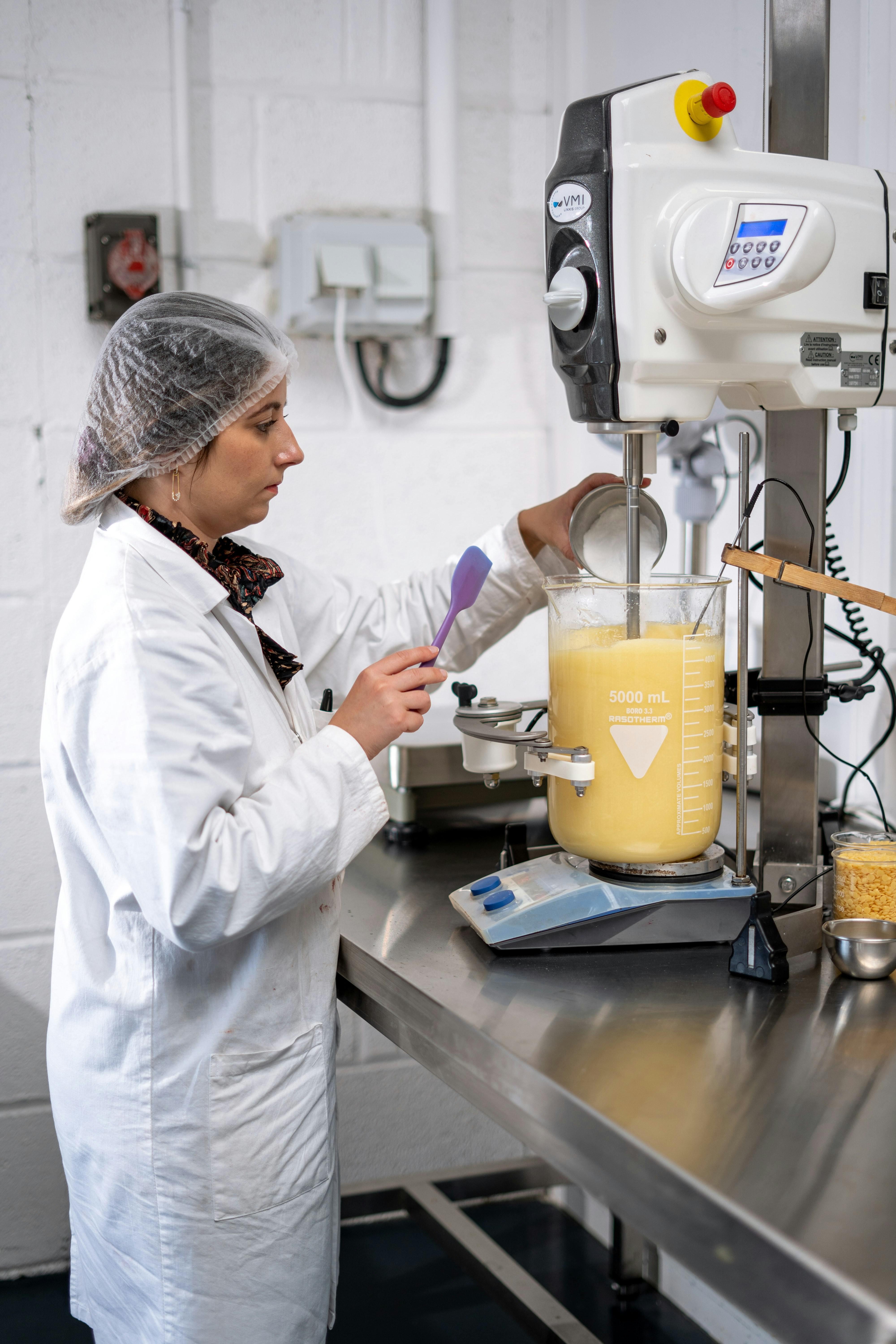 Scientist in a lab coat carefully measures liquid ingredients in a precision scale, showcasing the meticulous process of food formulation.