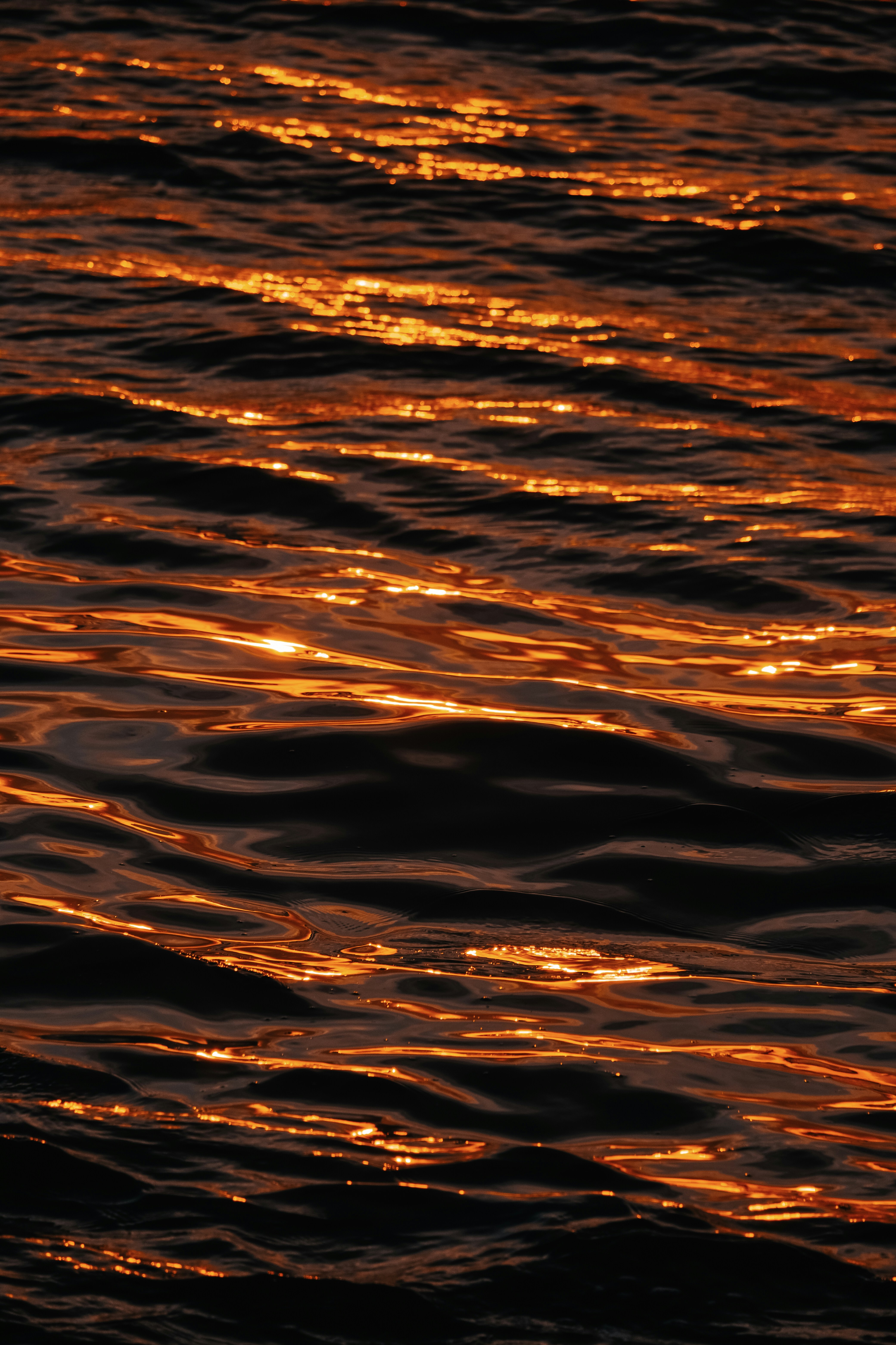 Ember Trails on Dark Tide: Sunset Light Leaks Across Rippling Water