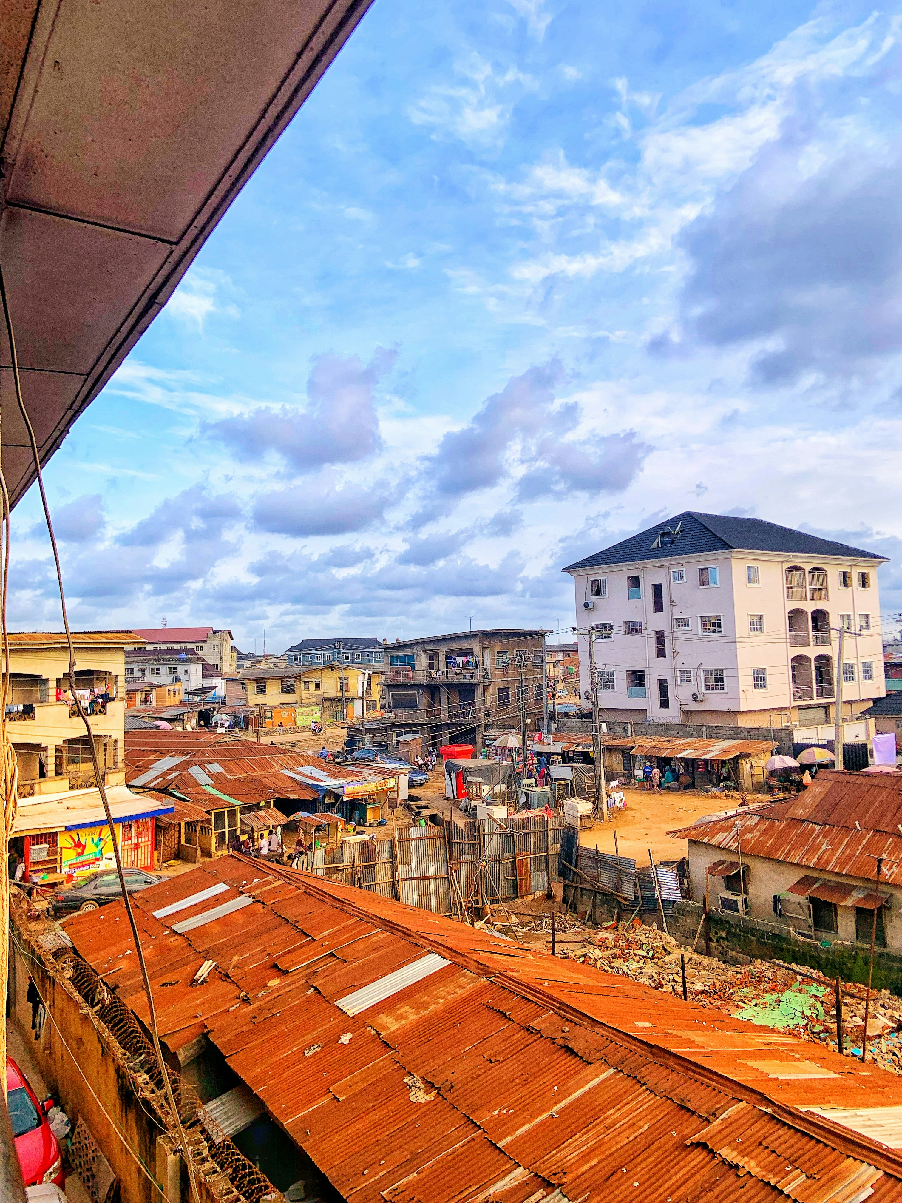 Vibrant marketplace scene with rusted rooftops and bustling activity under a cloudy sky. The layered architecture showcases the blend of residential and commercial spaces.