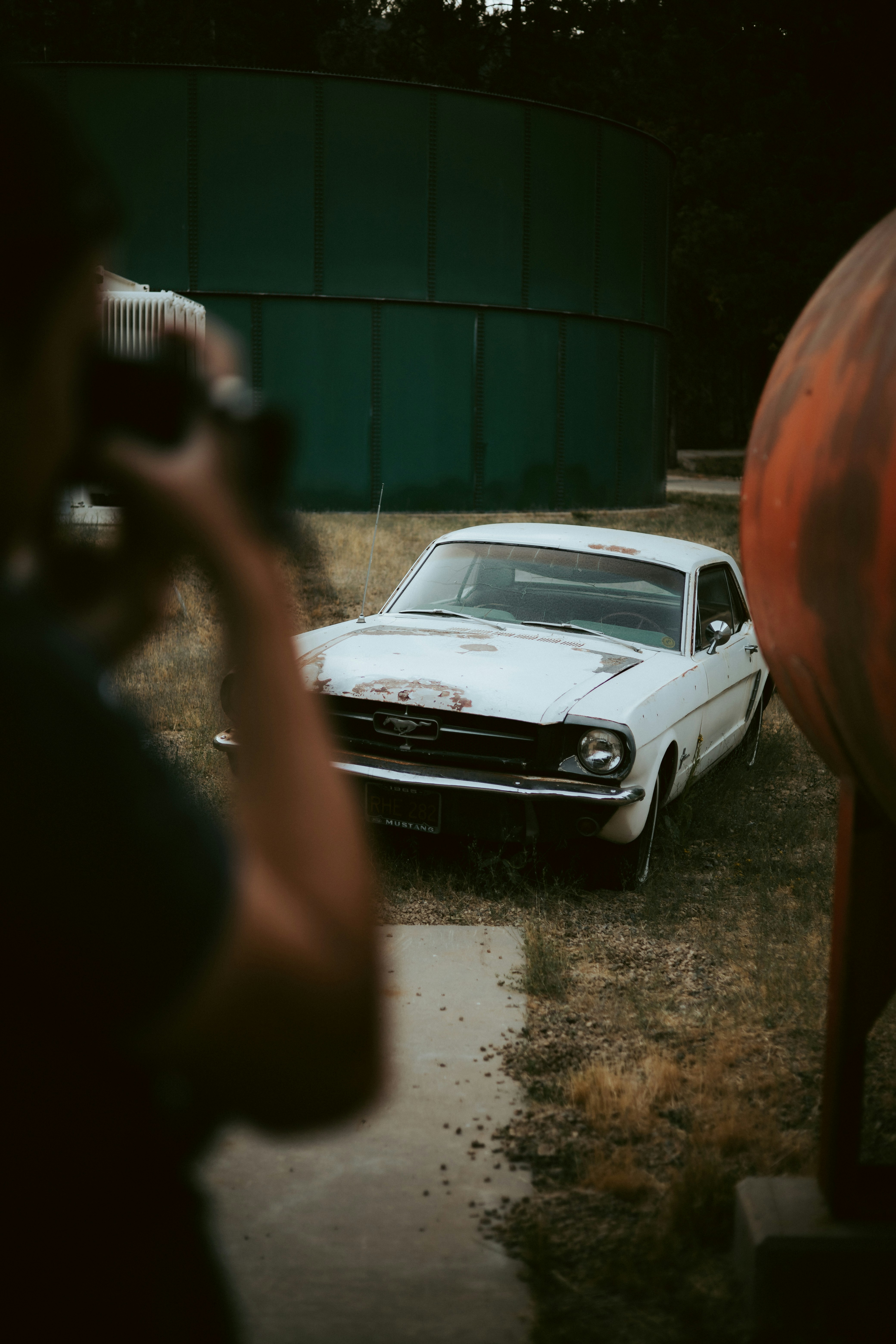 Rust and Reverie: A Weathered Mustang Between Industrial Giants