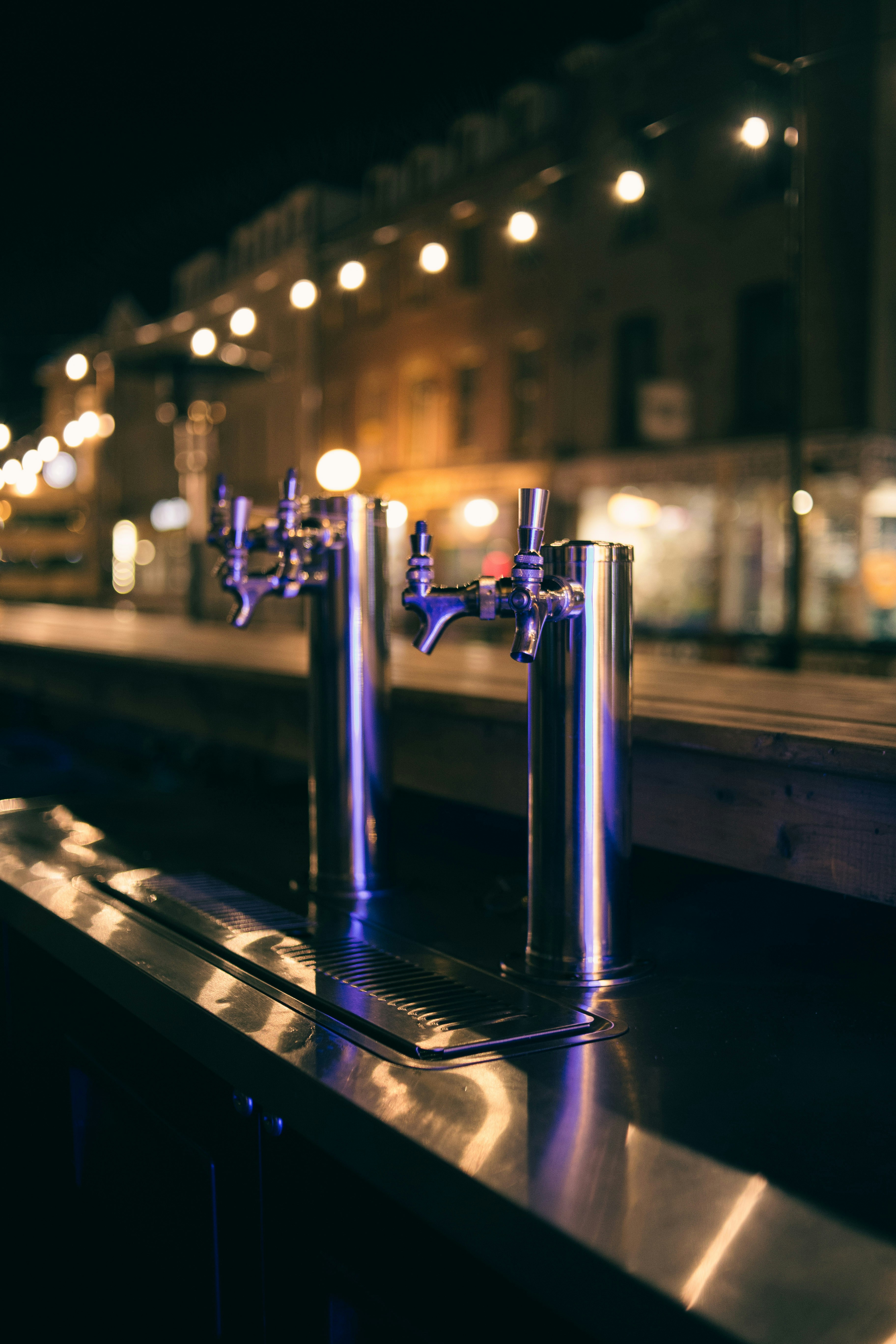 Shiny beer taps illuminated by ambient lights, showcasing a vibrant bar scene at night.