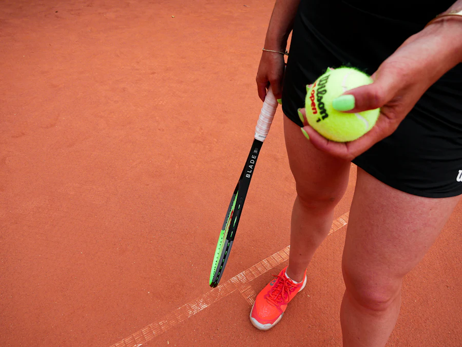 Player's hand holds a neon tennis ball and a Blade racket above a clay court baseline.